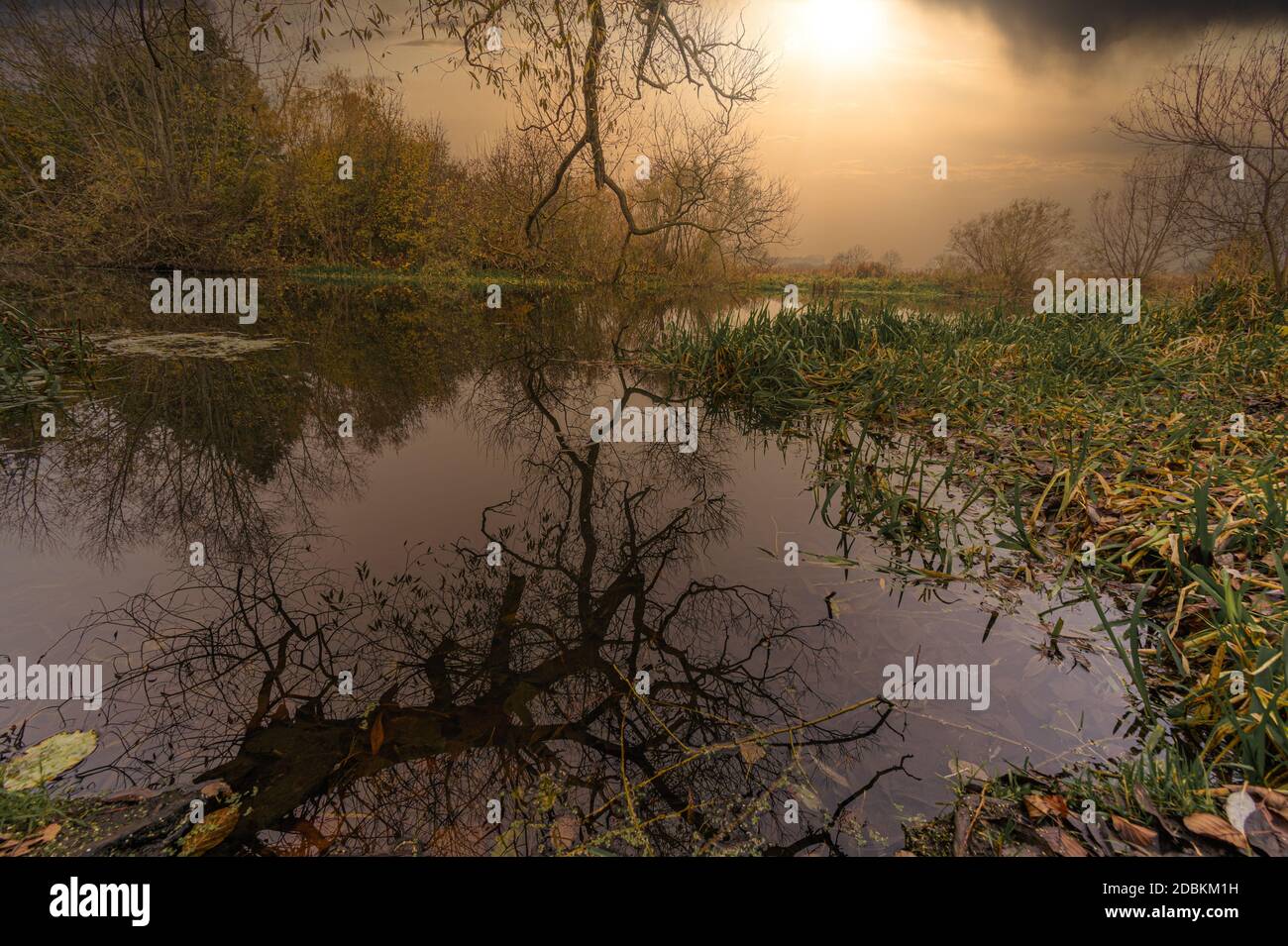 Reflections in a river with a dramatic sunset in the background ...