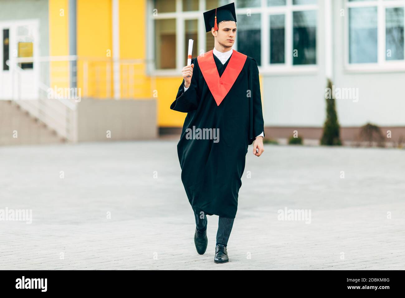 A male graduate student in a black graduation dress, walking with a ...