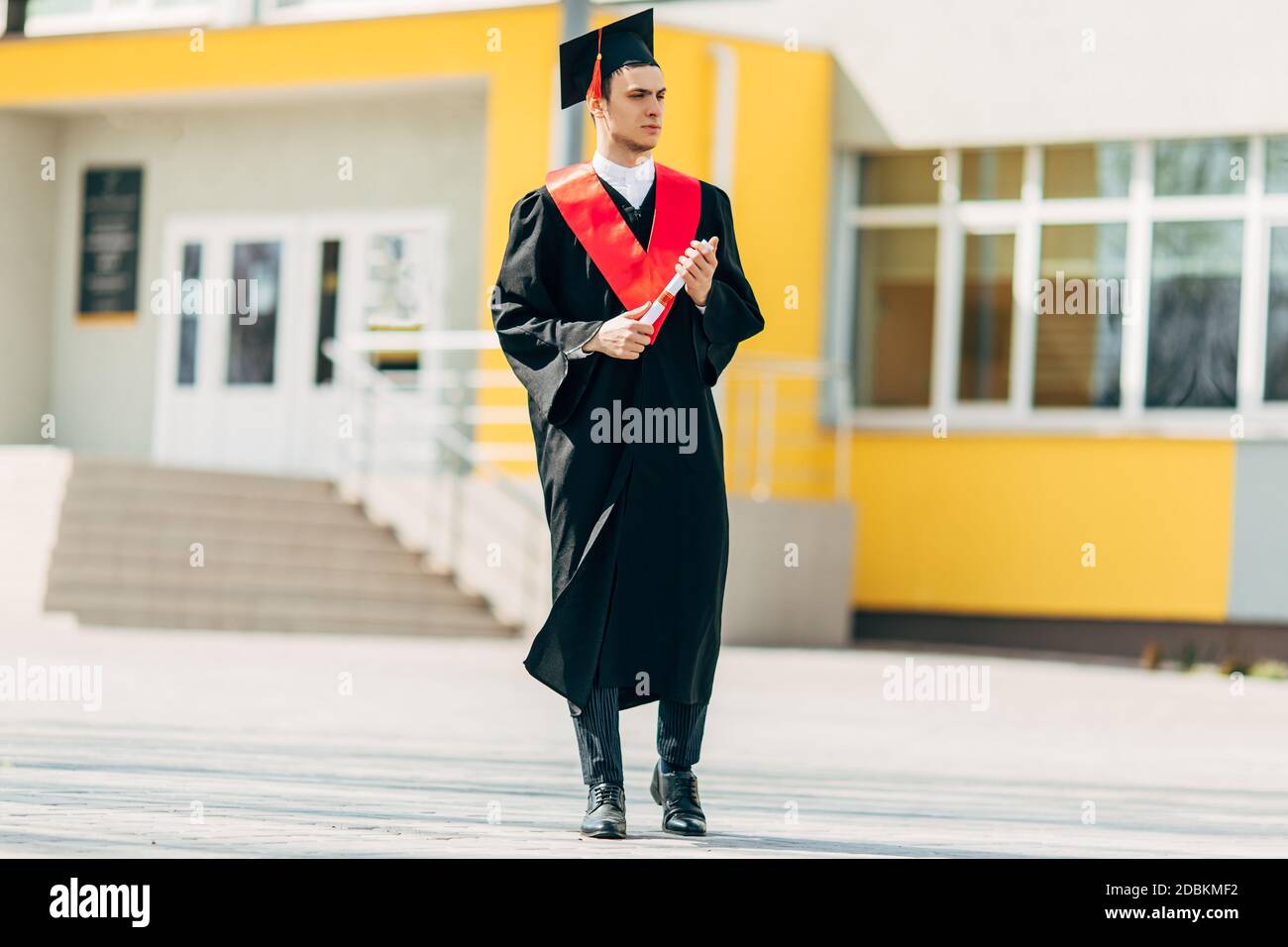 A male graduate student in a black graduation dress, walking with a ...