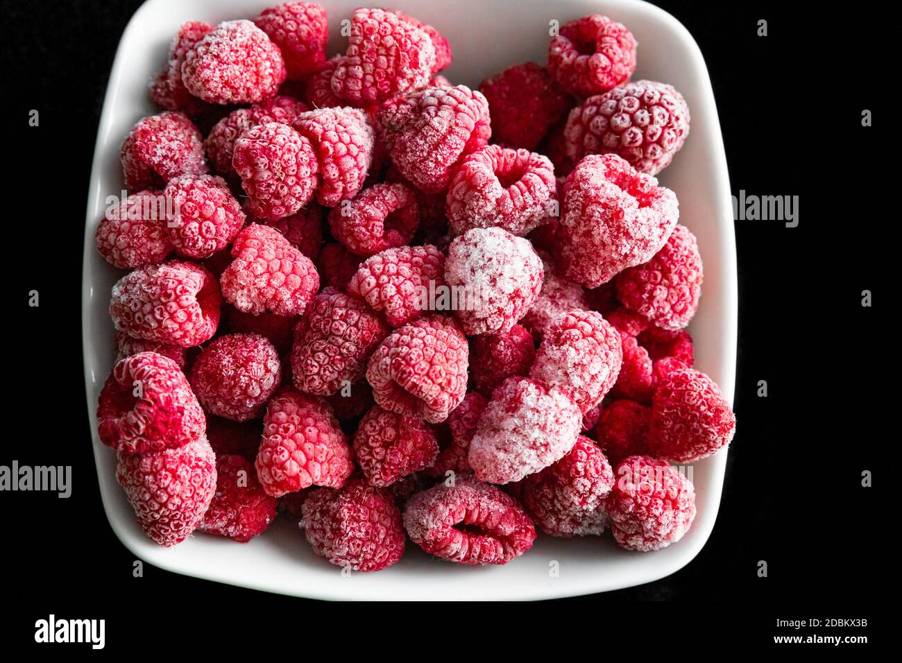 frozen ripe raspberries in a white deep plate on a black background ...