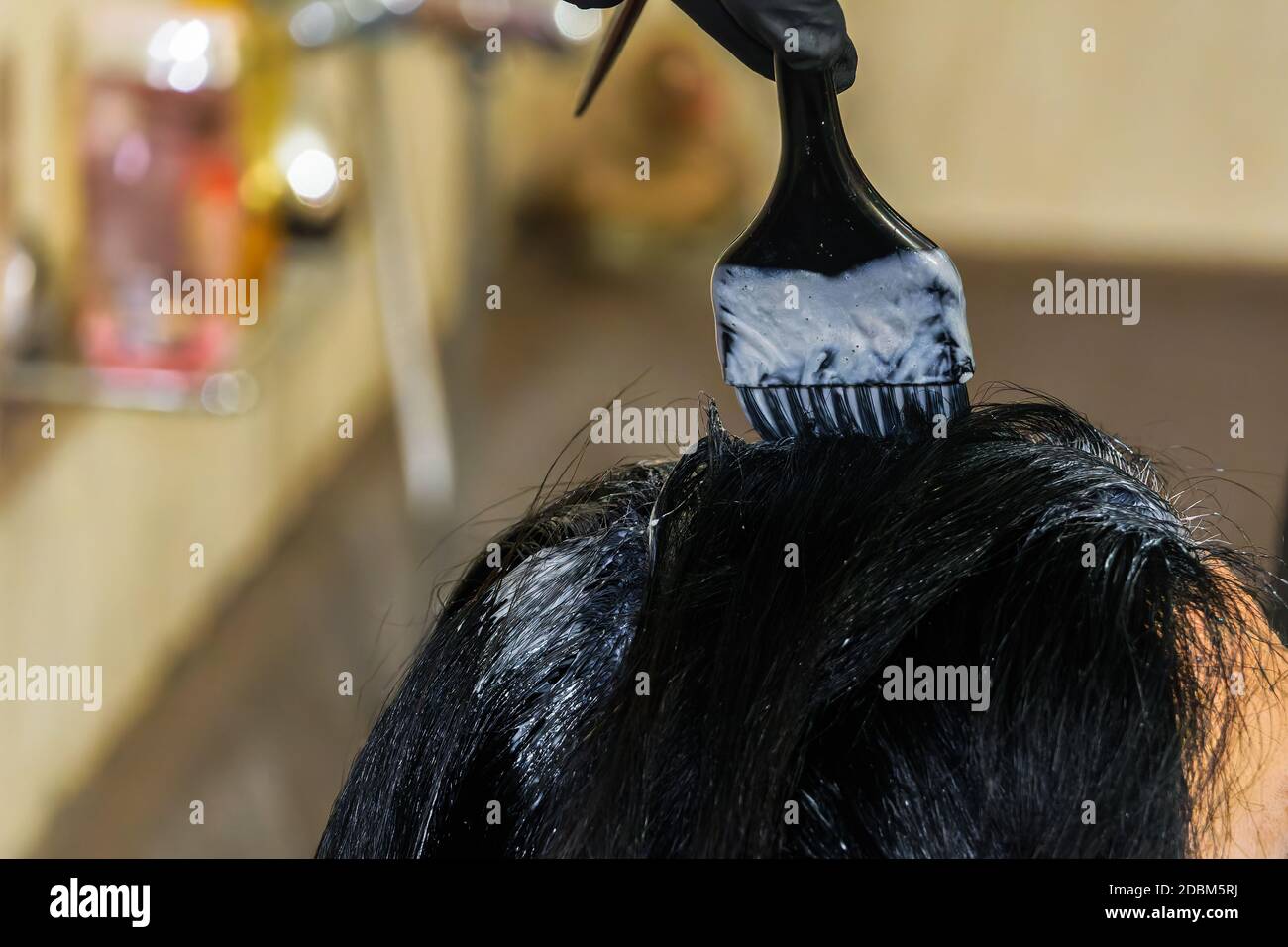 Hair dye color applied on the scalp by a hairdresser wearing black ...