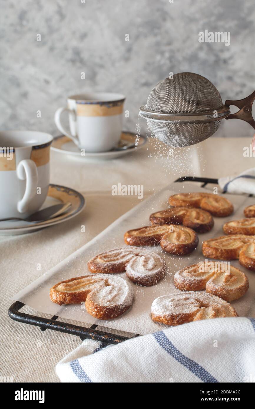 A lady sprinkle sugar powder from a sprinkler on top of the cookies ...