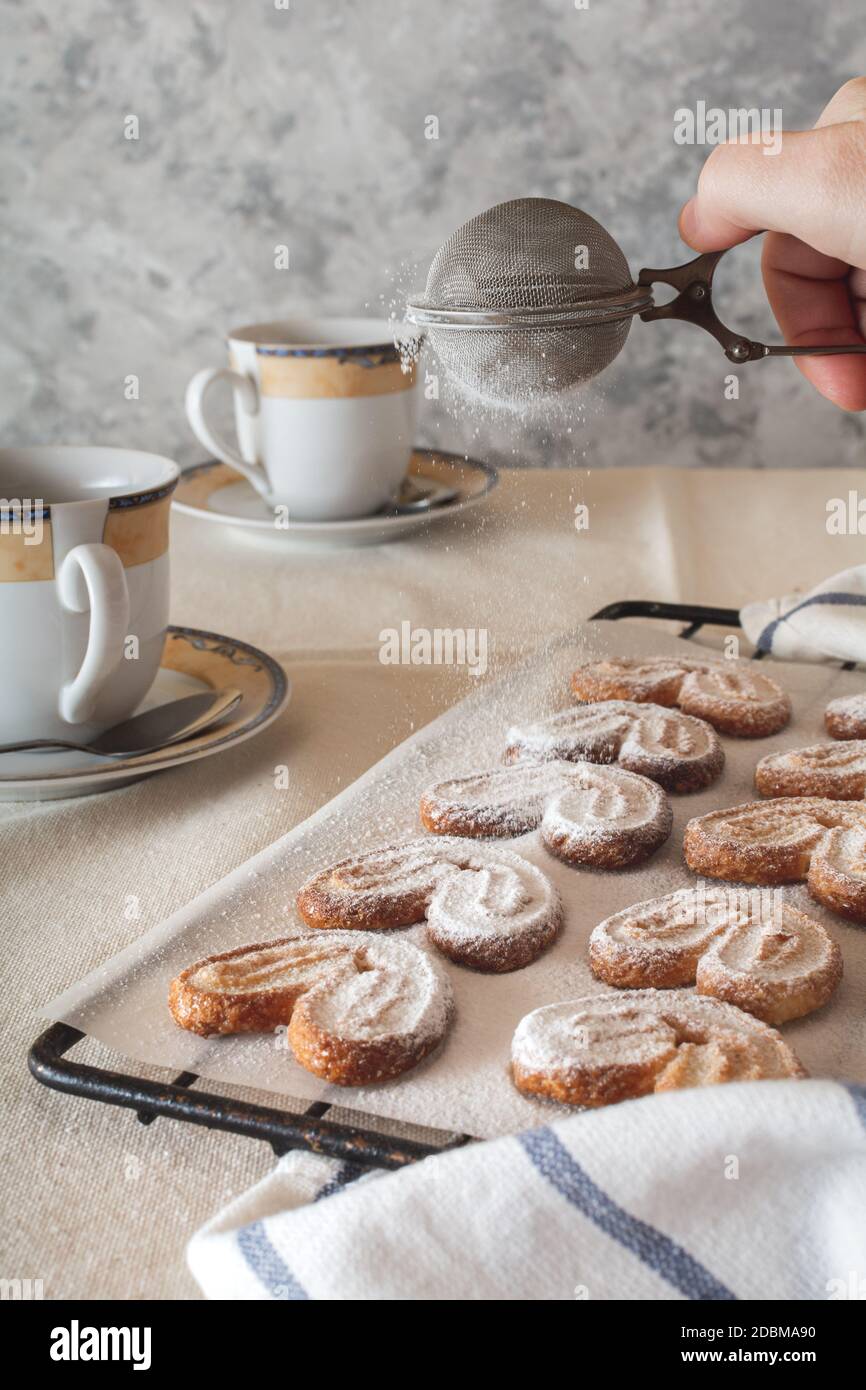 A lady sprinkle sugar powder from a sprinkler on top of the cookies ...