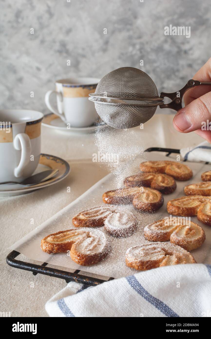A lady sprinkle sugar powder from a sprinkler on top of the cookies ...