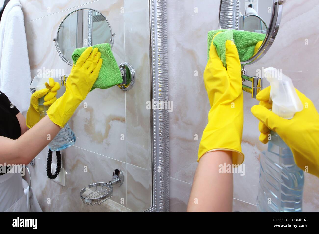 Hands in yellow gloves clean a small round mirror in the bathroom ...