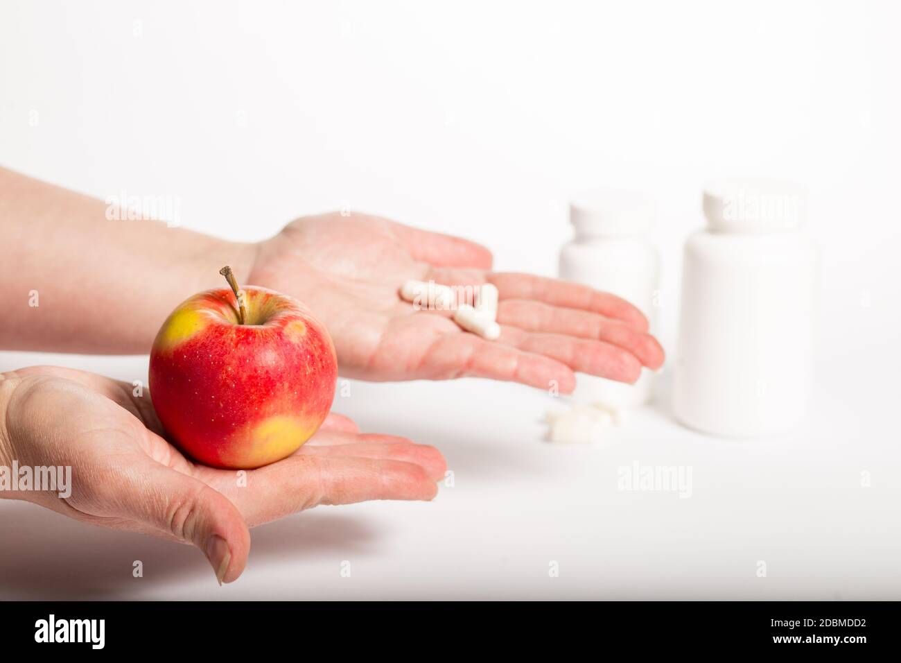 Red apple on a one hand and pills on another, on a white background ...