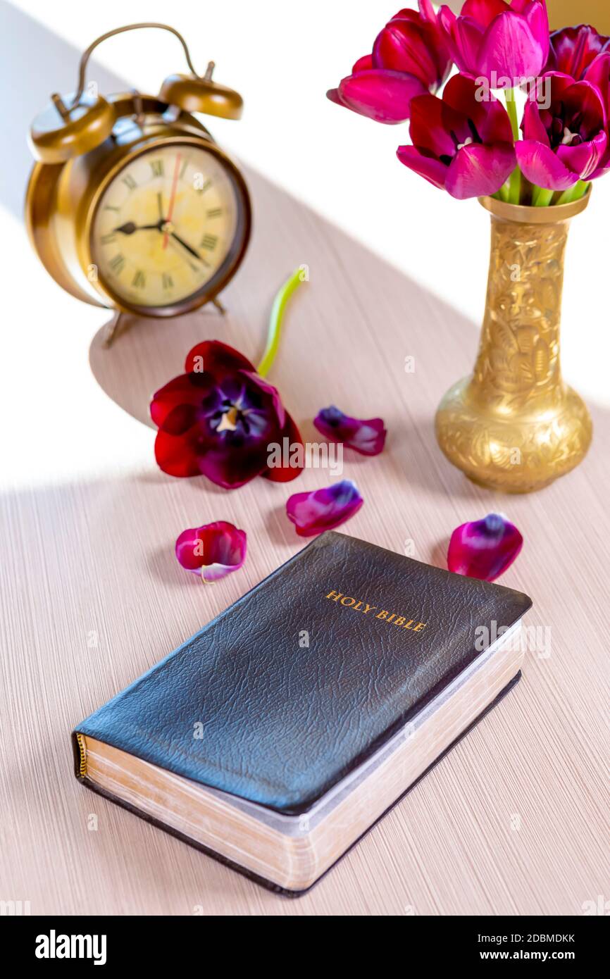 Holy Bible and old gold alarm clock with flowers on wooden table ...