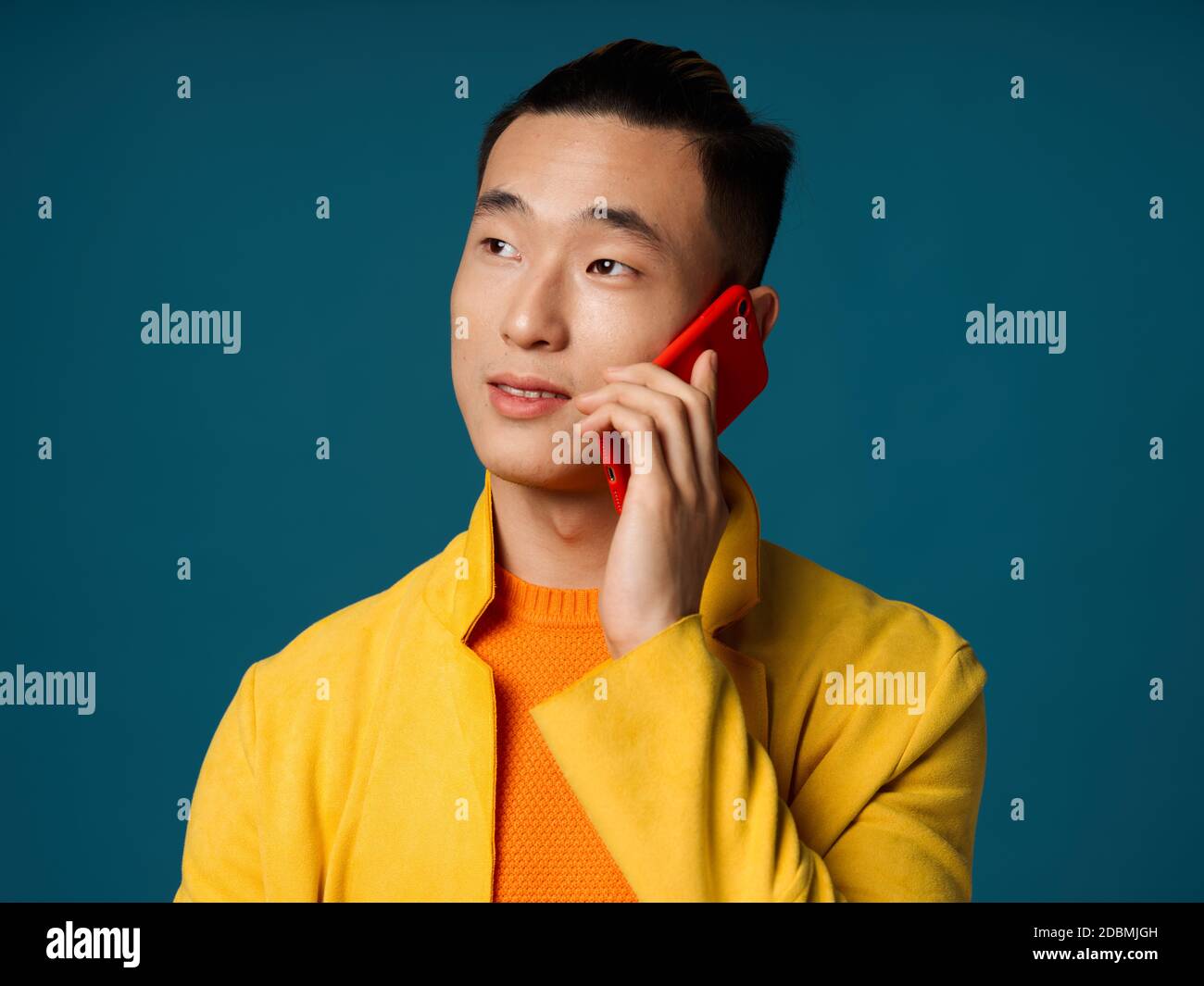 Asian guy in fashionable suit talking on the phone on a blue background ...