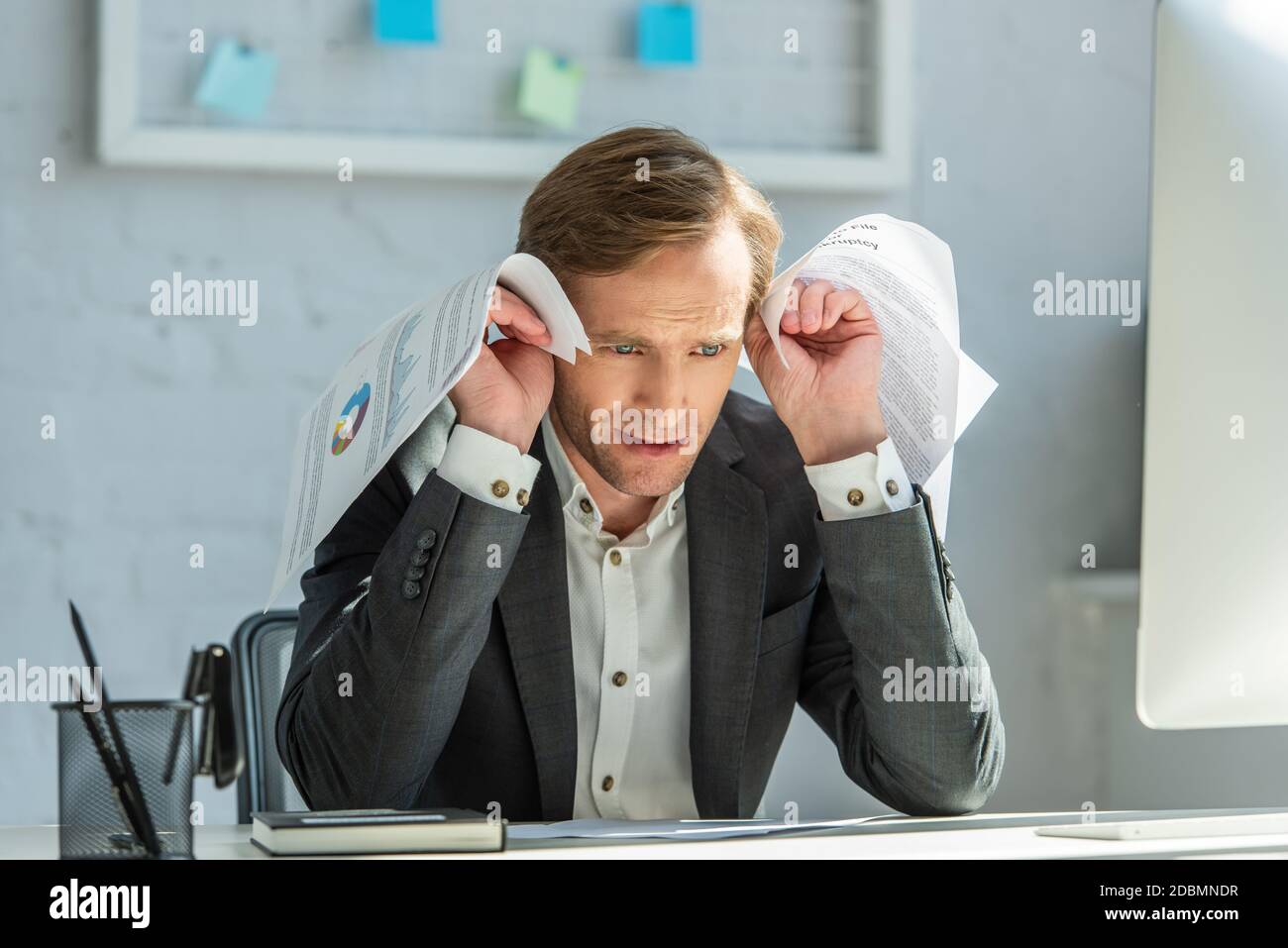 Frustrated businessman holding documents, while sitting at workplace ...