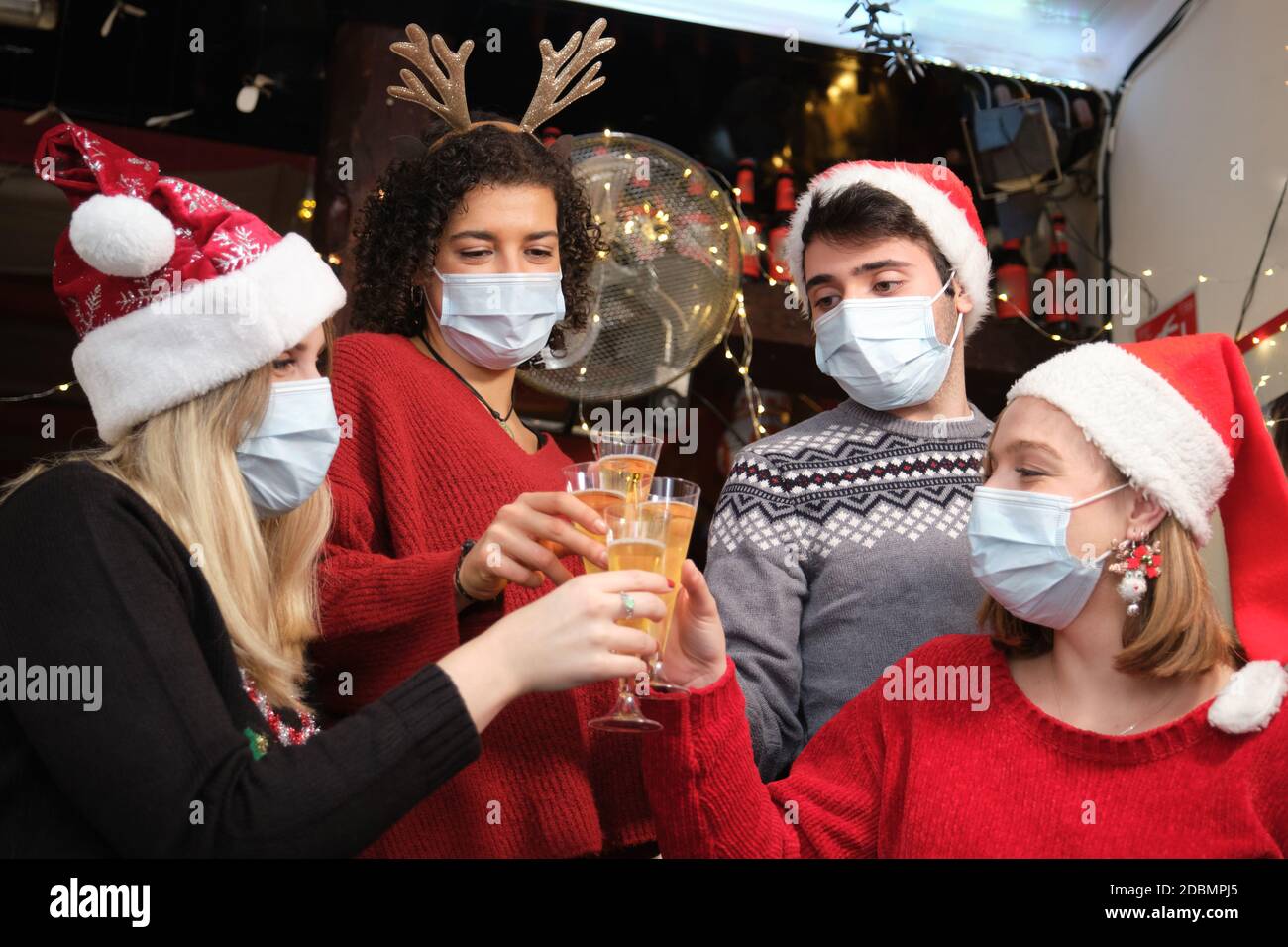 Friends wearing face masks at a Christmas party making a toast in a bar ...