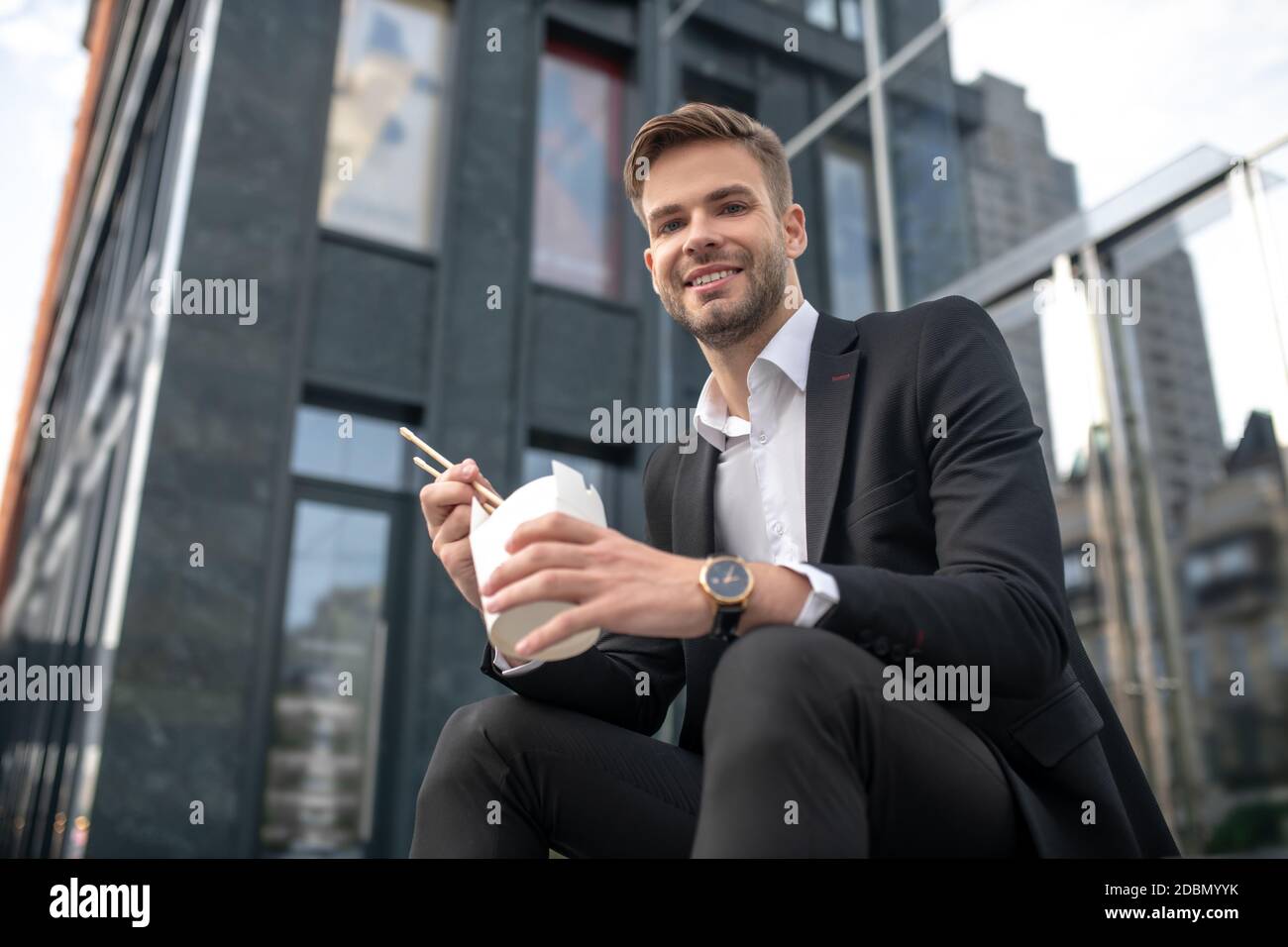 Smiling man sitting on the steps and eating asian food Stock Photo - Alamy