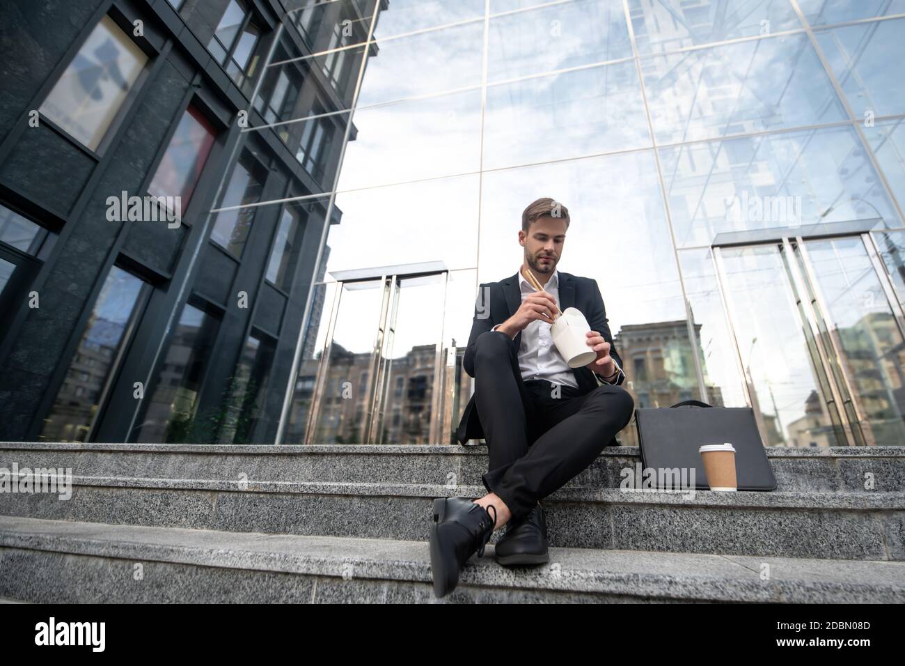 A young man sitting on the steps and eating asian food Stock Photo - Alamy