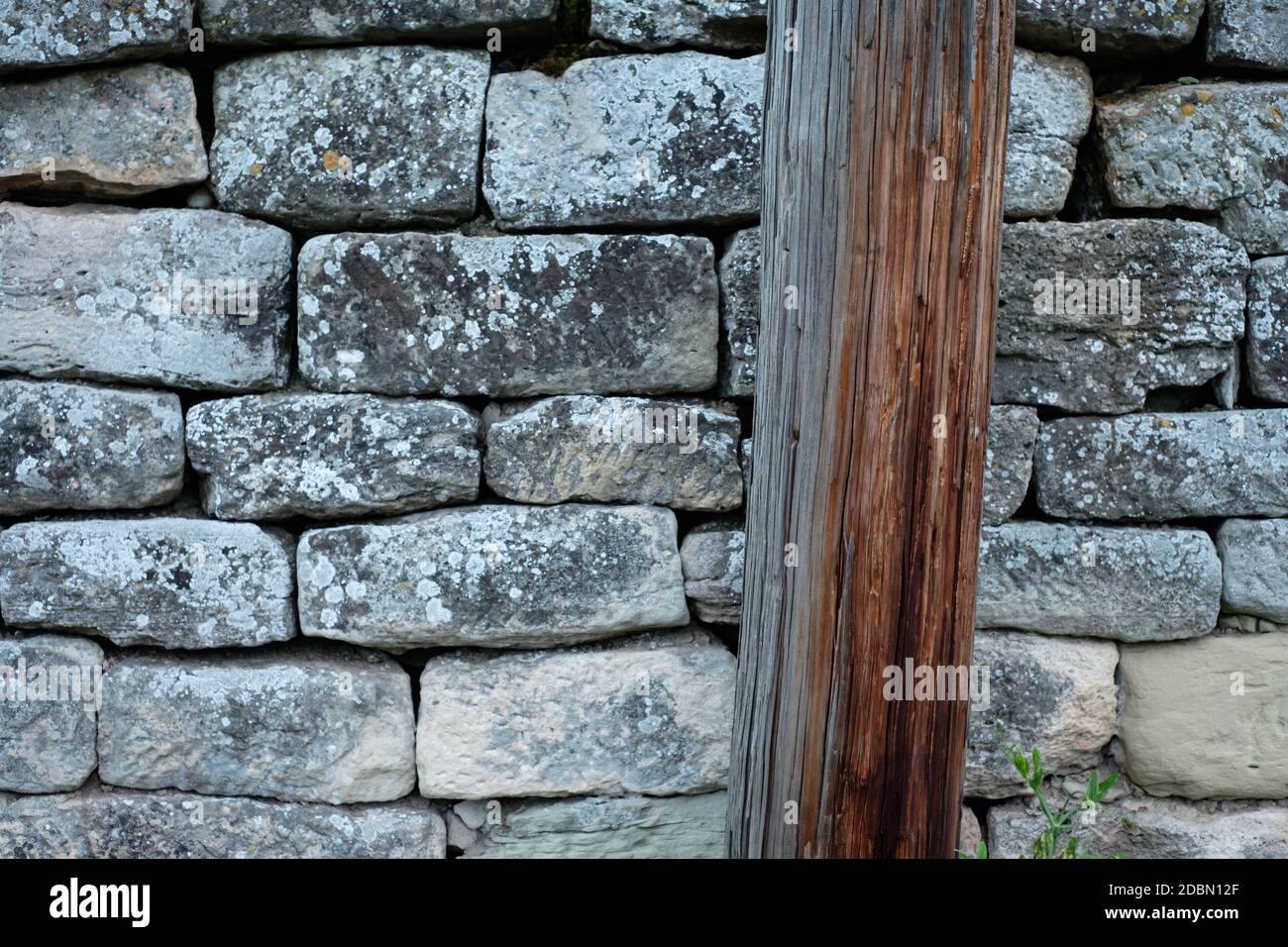 Wooden post in front of stone wall closeup Stock Photo - Alamy