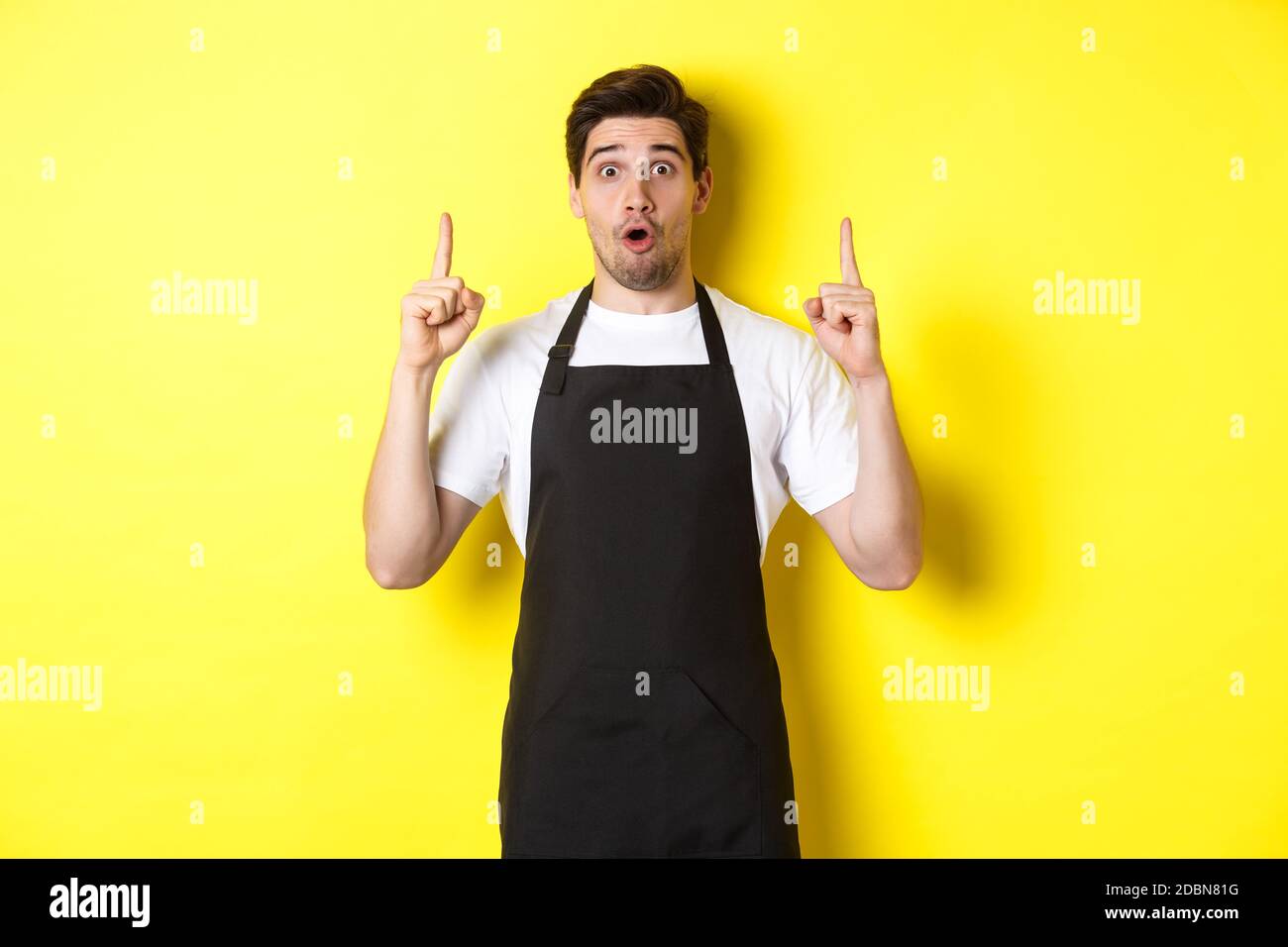 Surprised male waiter in black apron showing logo or advertisement ...
