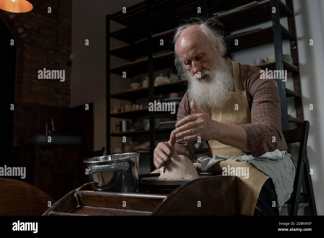 High angle of craftsman working on pottery wheel while sculping from ...