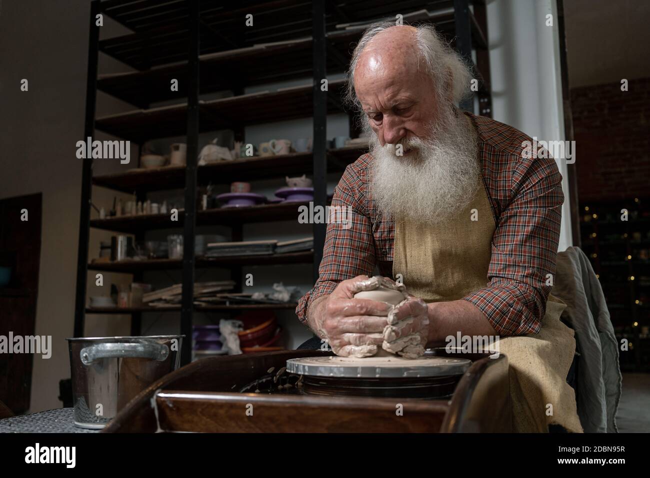 High angle of craftsman working on pottery wheel while sculping from ...