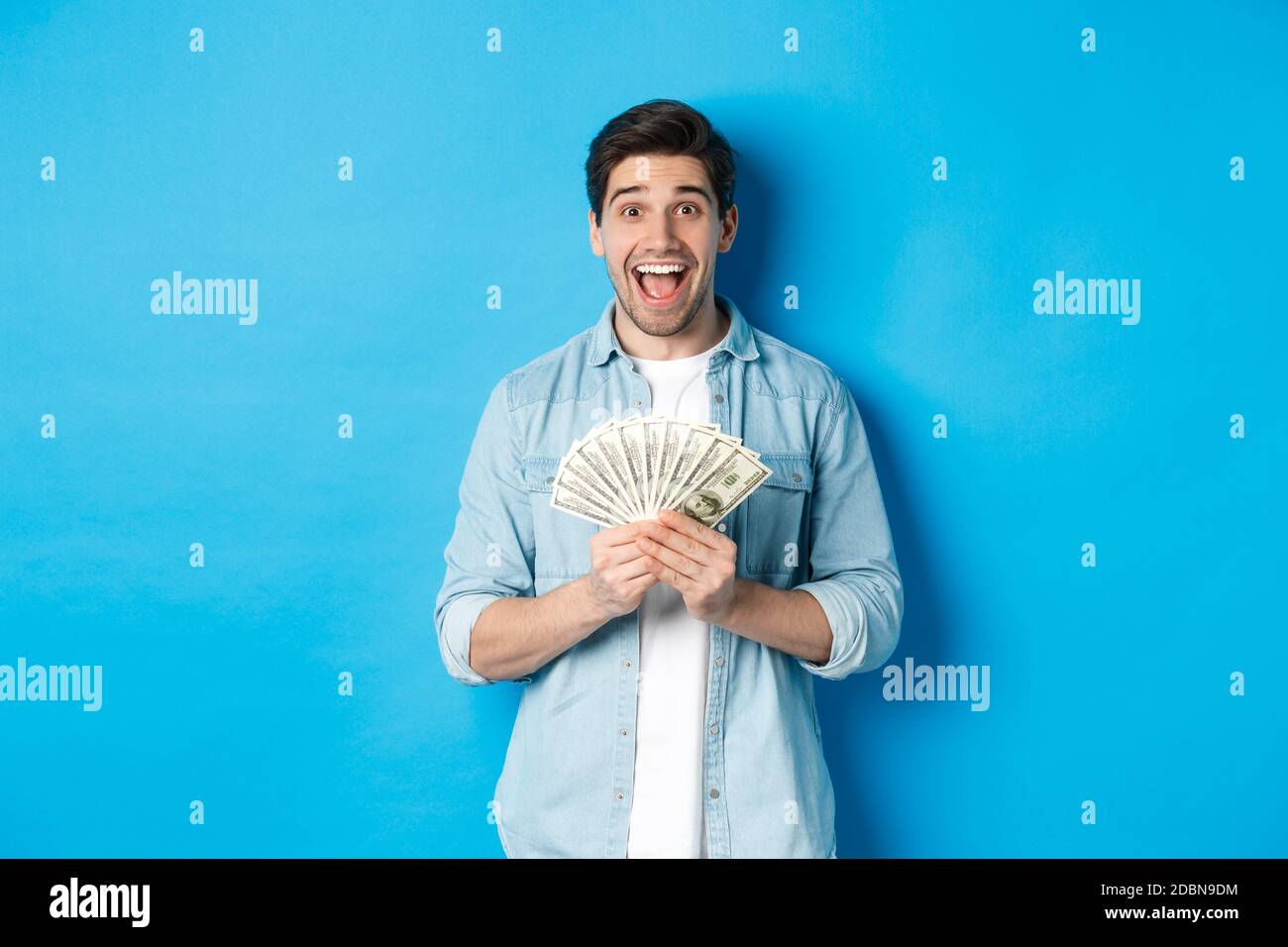 Excited and surprised attractive man, holding money prize and smiling ...