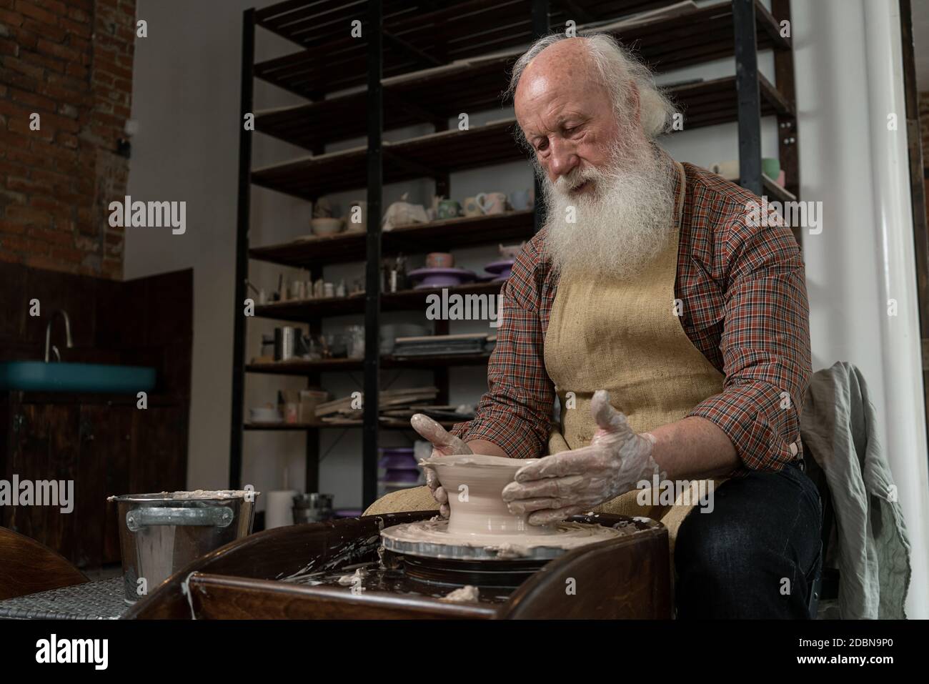 High angle of craftsman working on pottery wheel while sculping from ...