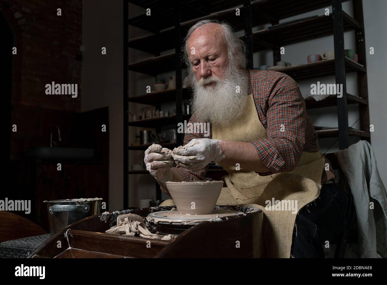 High angle of craftsman working on pottery wheel while sculping from ...