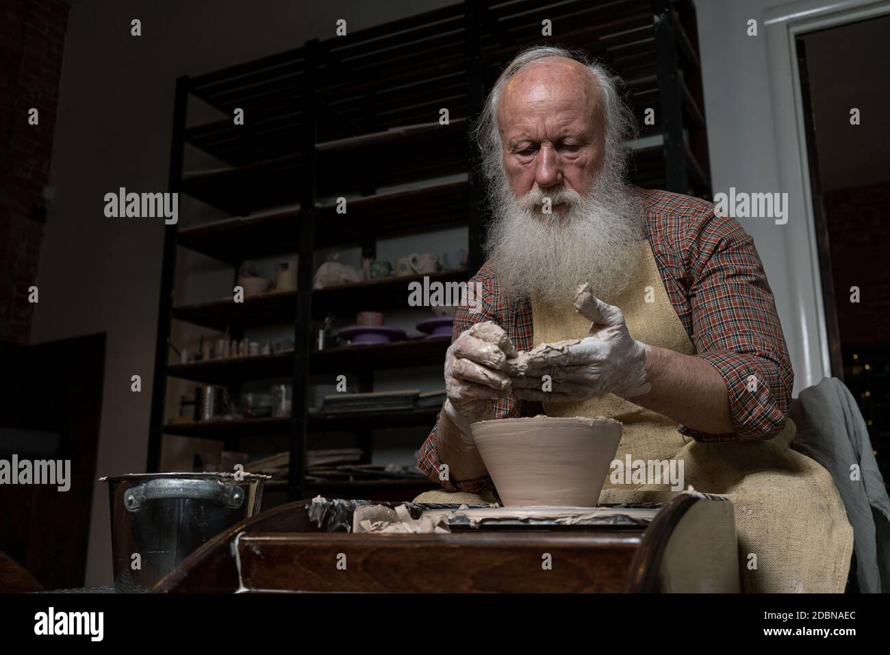 High angle of craftsman working on pottery wheel while sculping from ...