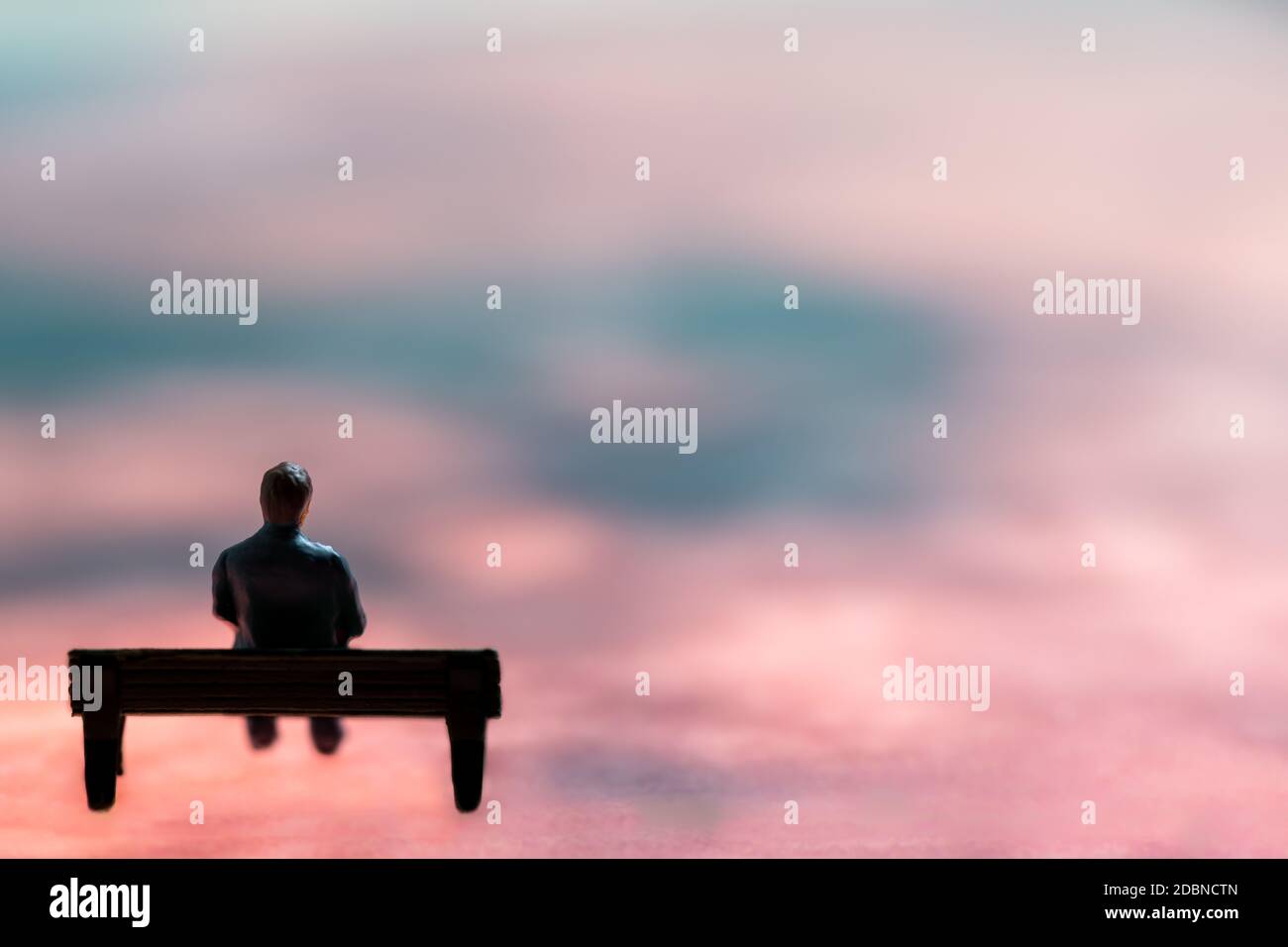 Miniature figurine posed as man sitting alone on a bench in surreal ...