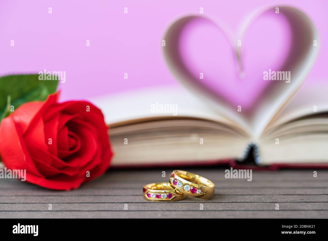 Pages of book curved into a heart shape with red rose and wedding ring ...
