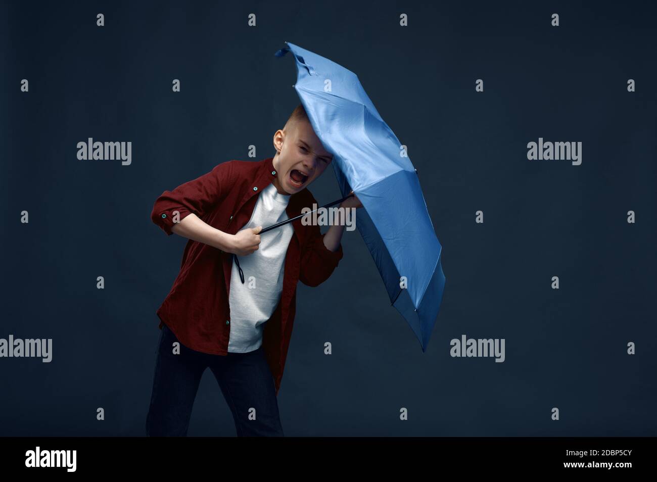 Little boy with a scared face holds an umbrella in studio, wind effect ...