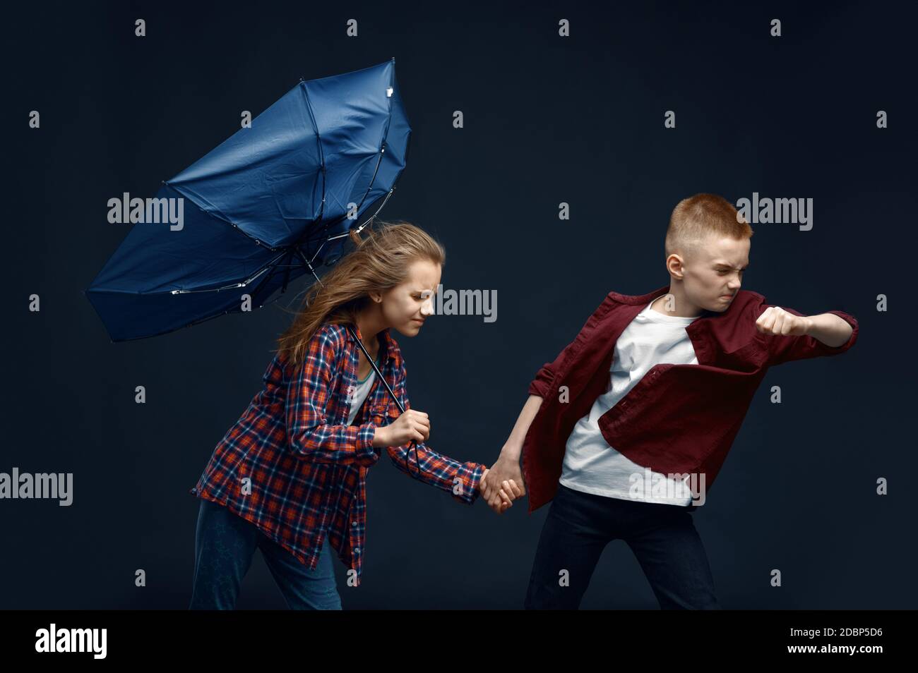 Little boy and girl with umbrella against powerful airflow in studio ...