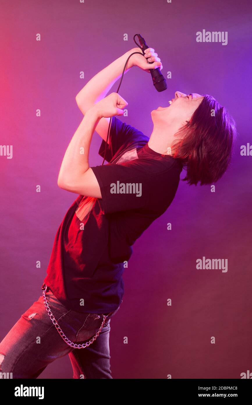 The young guy is singing and screaming in microphone on stage, concert ...