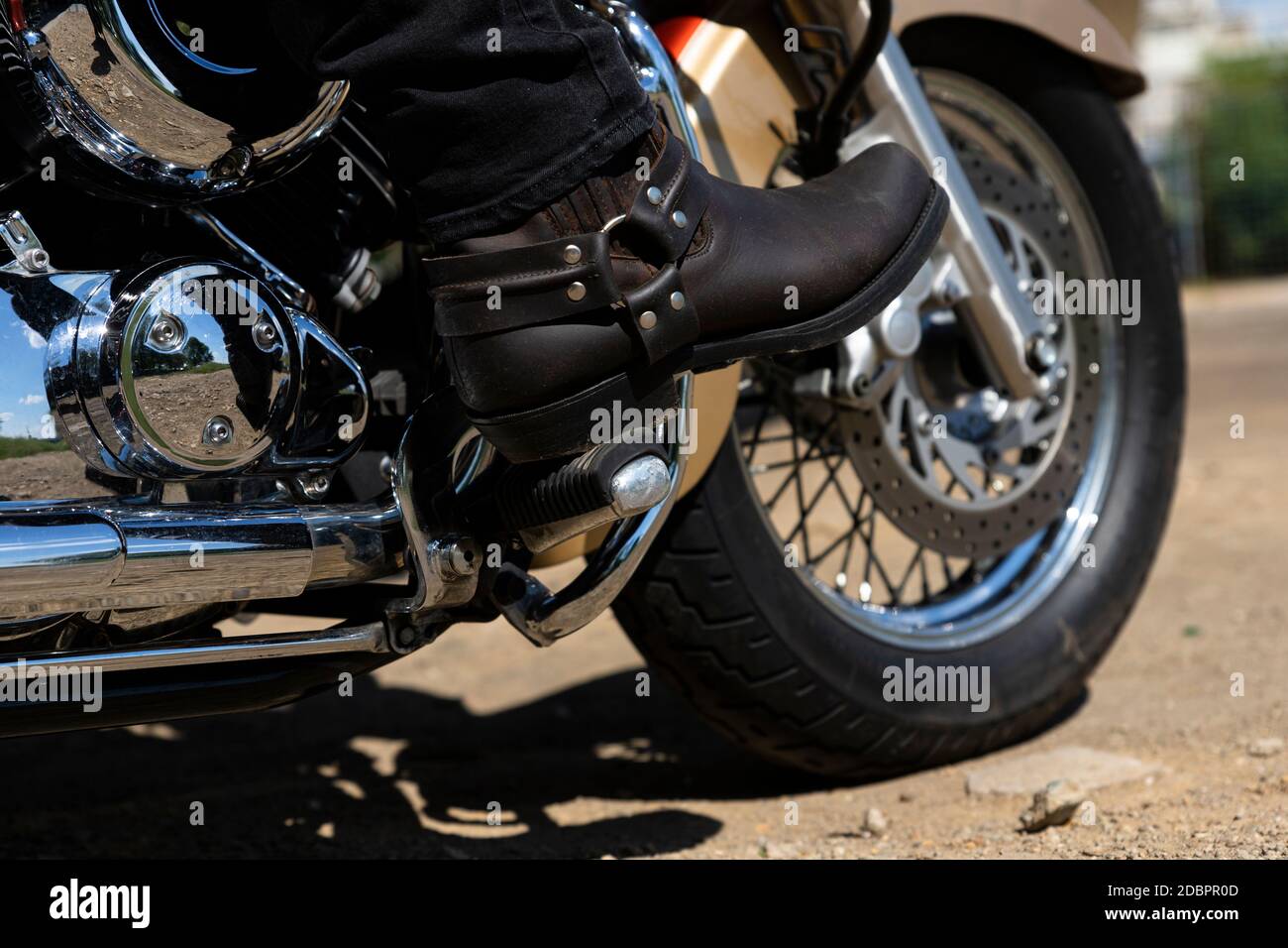 Biker riding a motorcycle. Bottom view of the legs in leather cowboy ...