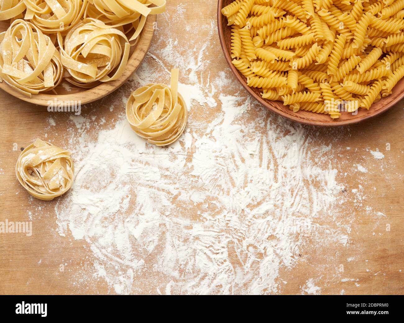 raw fusilli and fettuccine pasta in wooden plates on a brown wooden ...