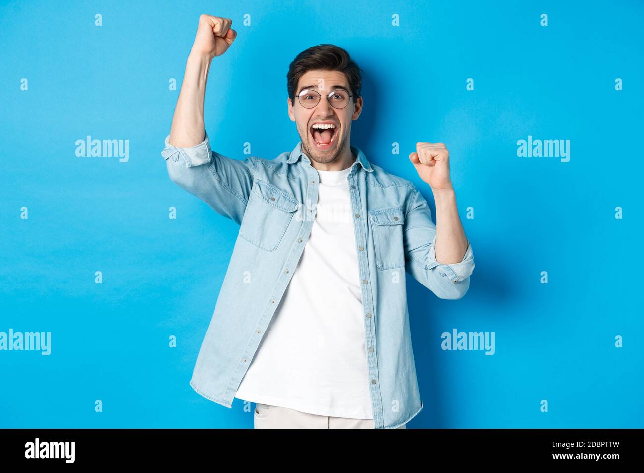 Excited handsome man triumphing, raising hands up and shouting for joy ...