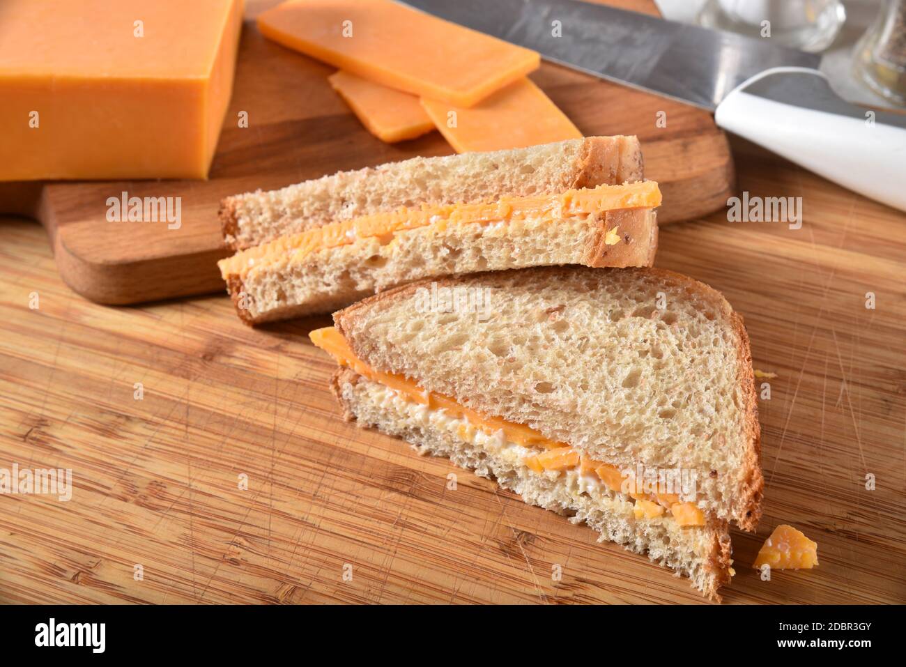A cheddar cheese sandwich on a cutting board with a block of cheese ...