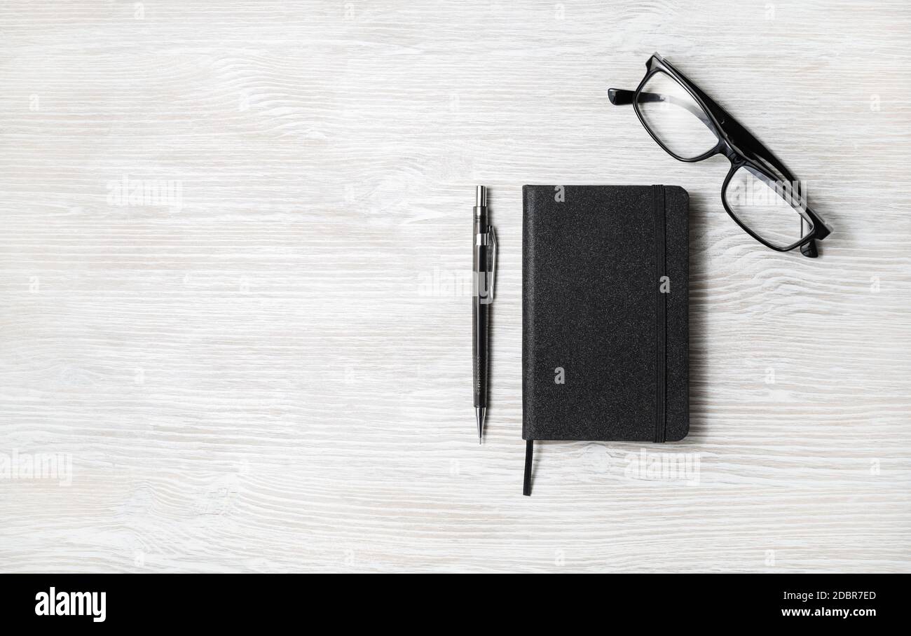 Black notepad, glasses and pencil on light wood table background. Copy ...