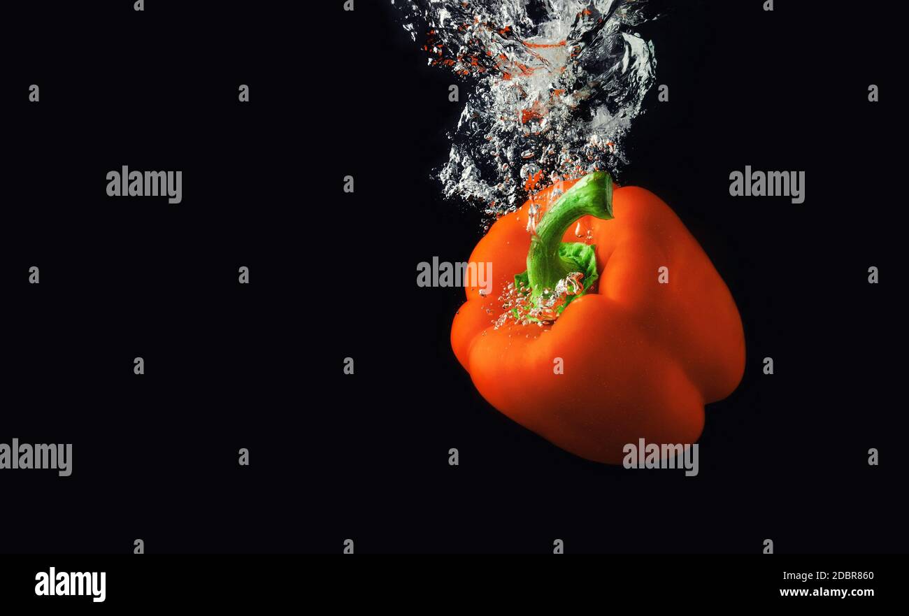 Red paprika falling into the water with a splash and air bubbles ...