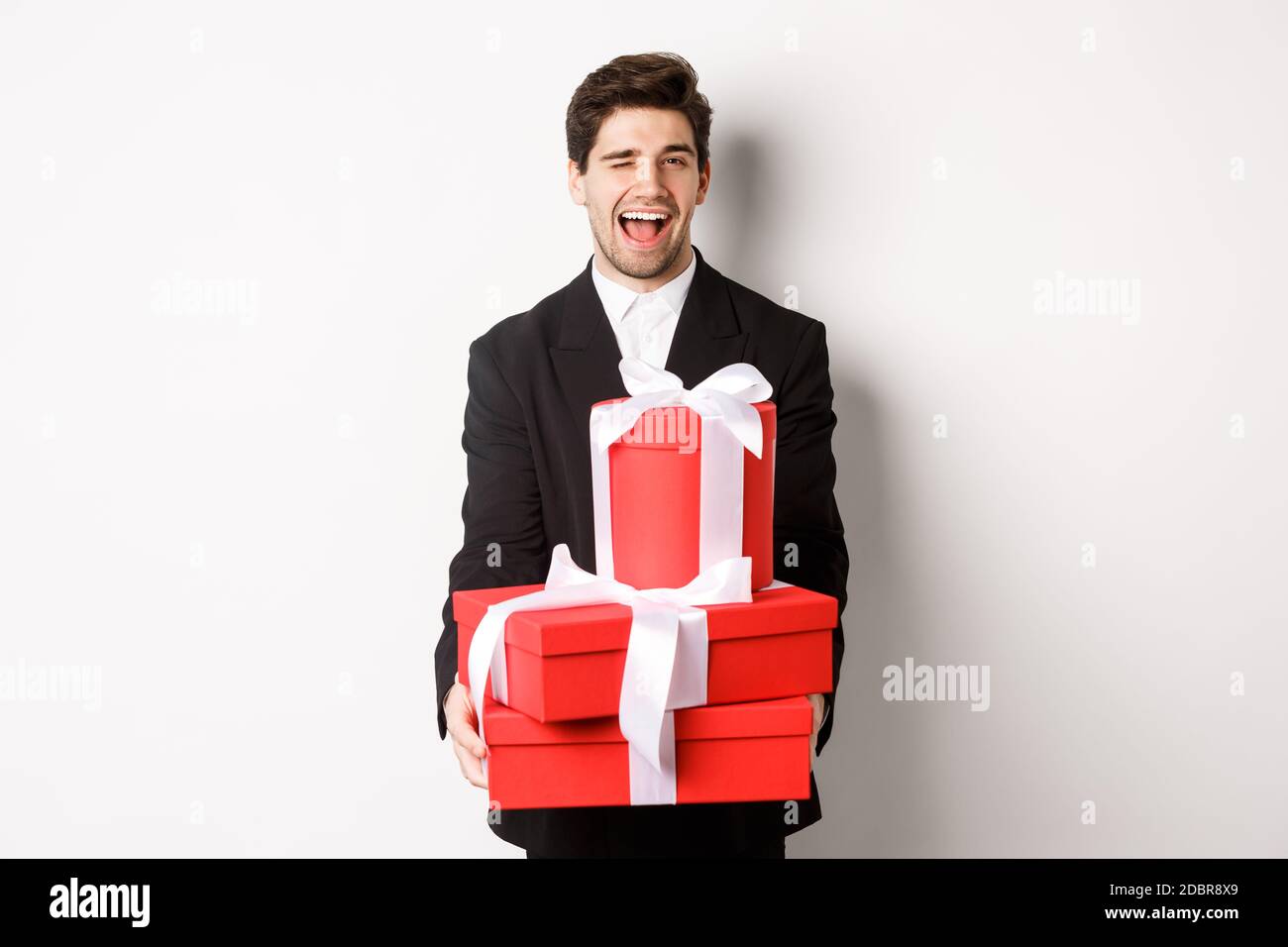 Image of handsome guy in black suit, holding gifts and winking at ...