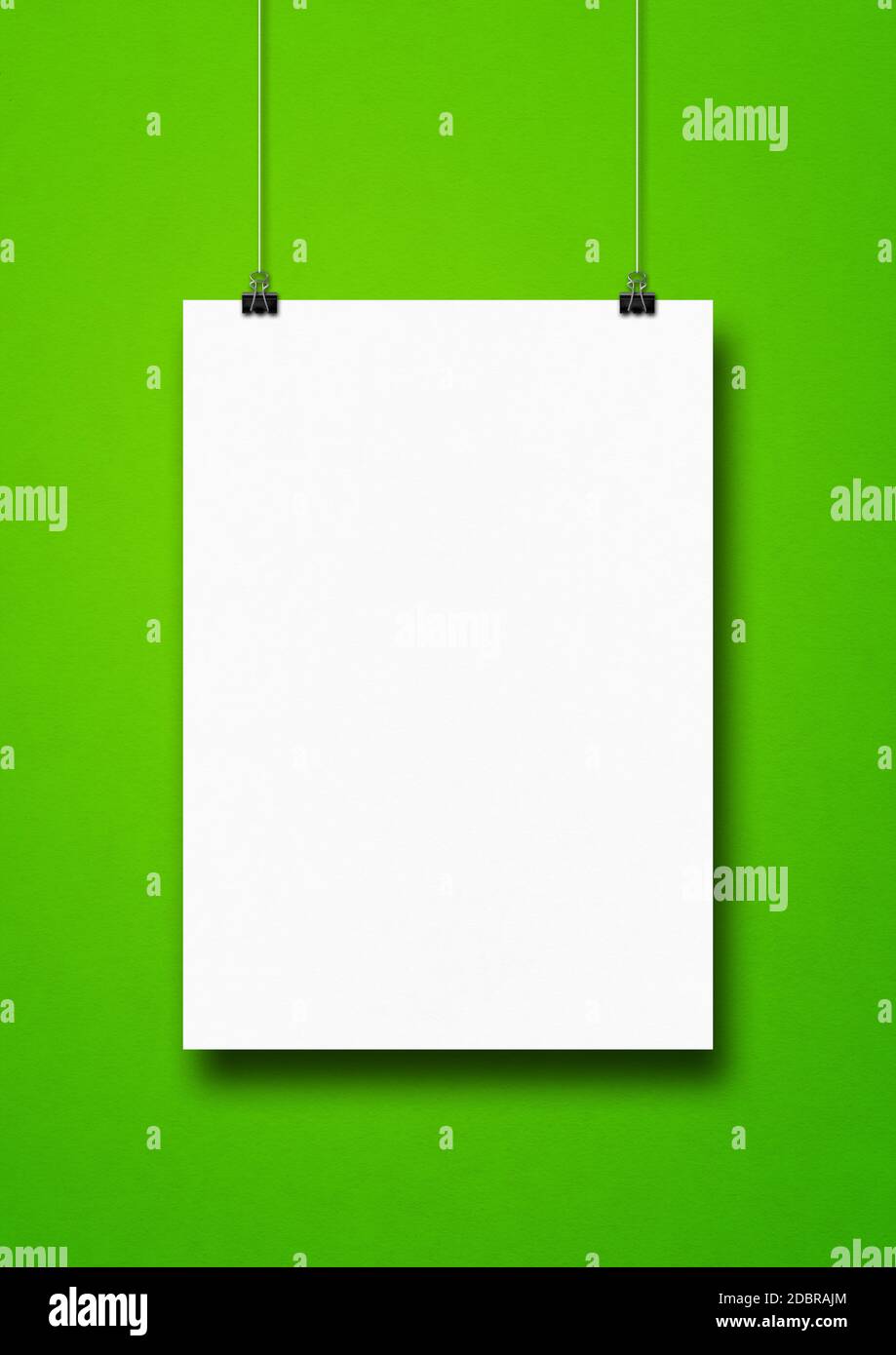 White poster hanging on a green wall with clips. Blank mockup template ...