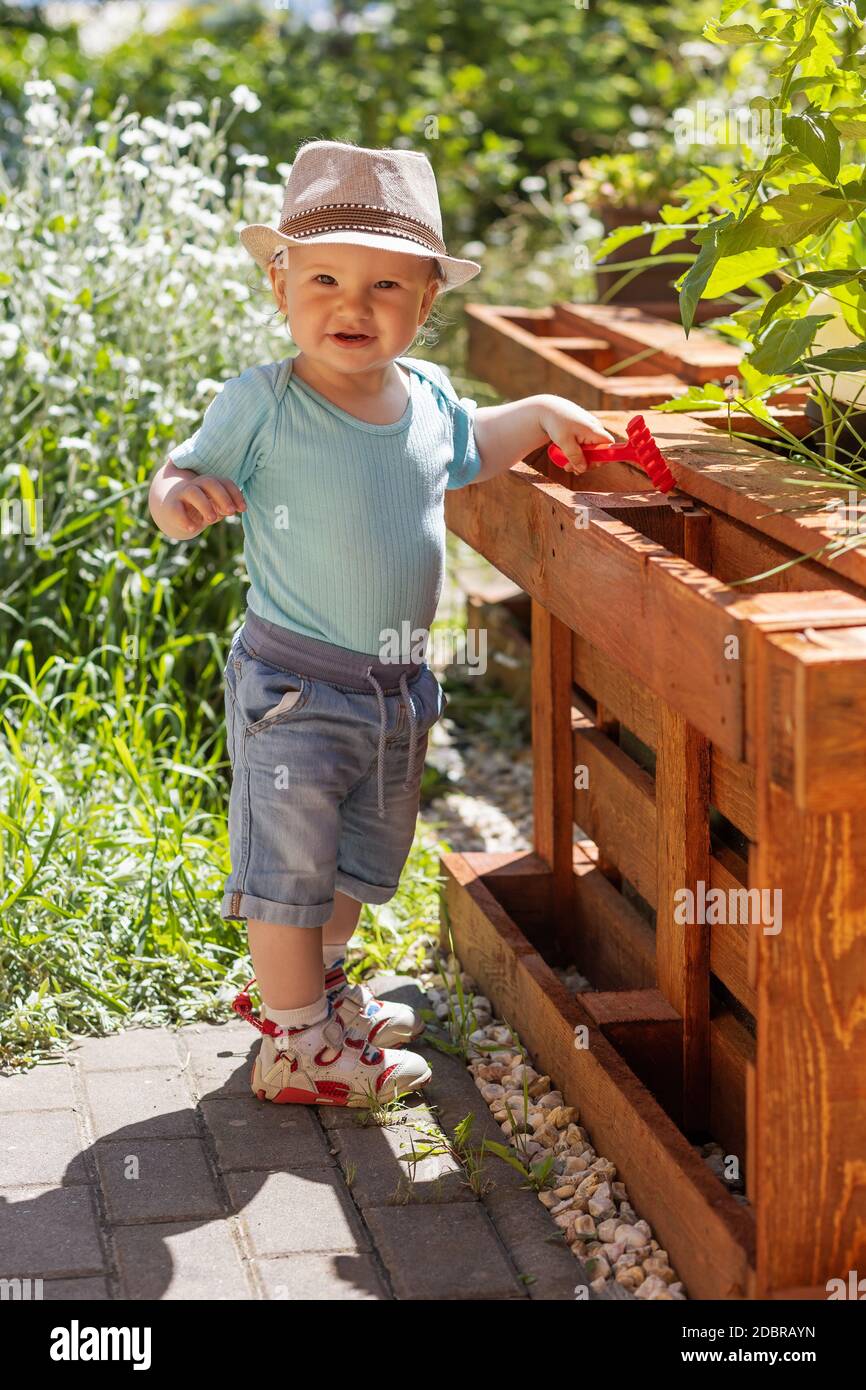 Smiling baby boy is posing next to raised flower bed holding red baby ...
