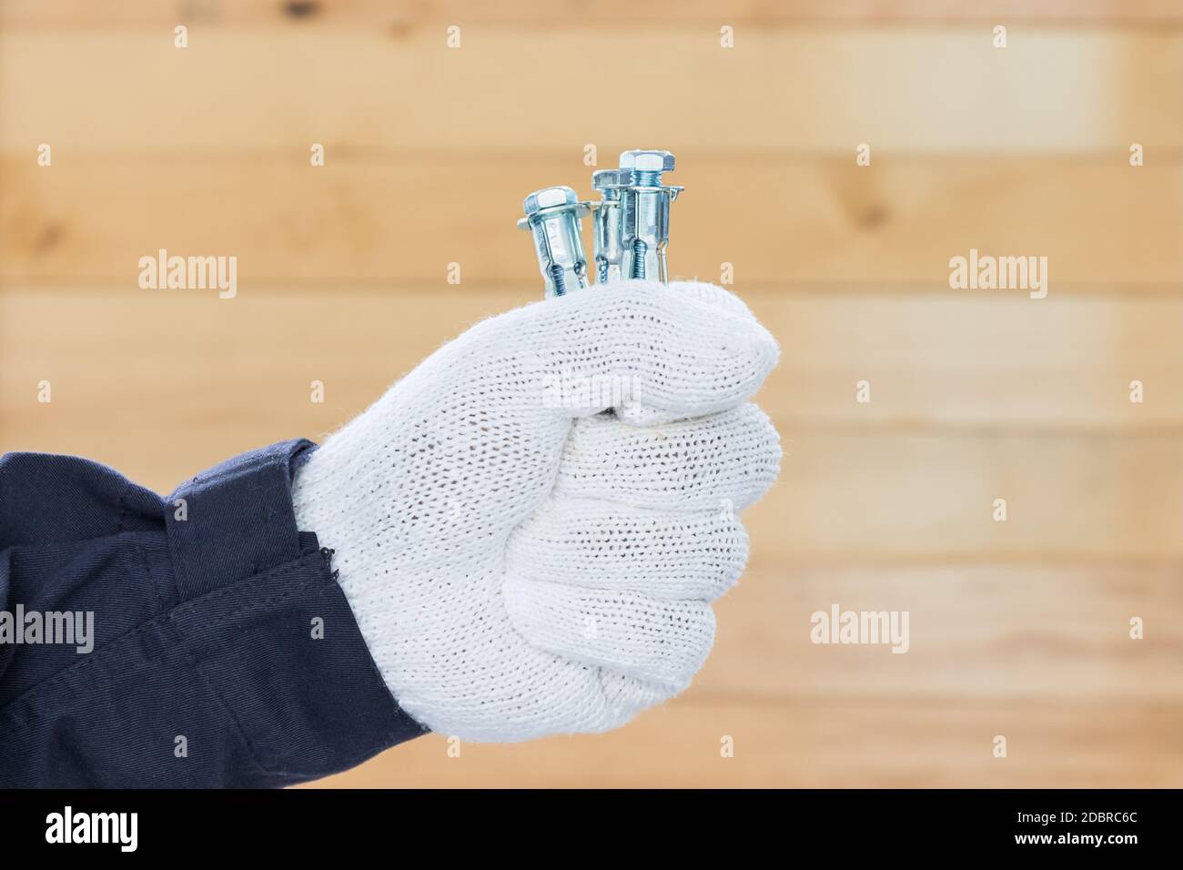 Working hand in glove holding metal anchor bolts with wall wood ...