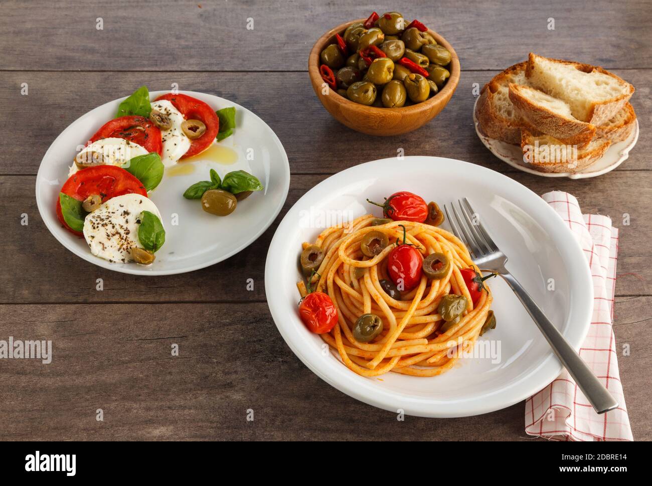 Full table of italian meals on plates. Spaghetti, caprese, olives and ...
