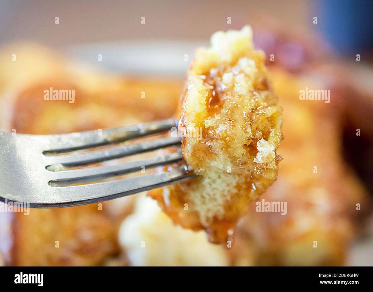 Bite sized piece of French Toast on a fork. The remainder of the plate ...