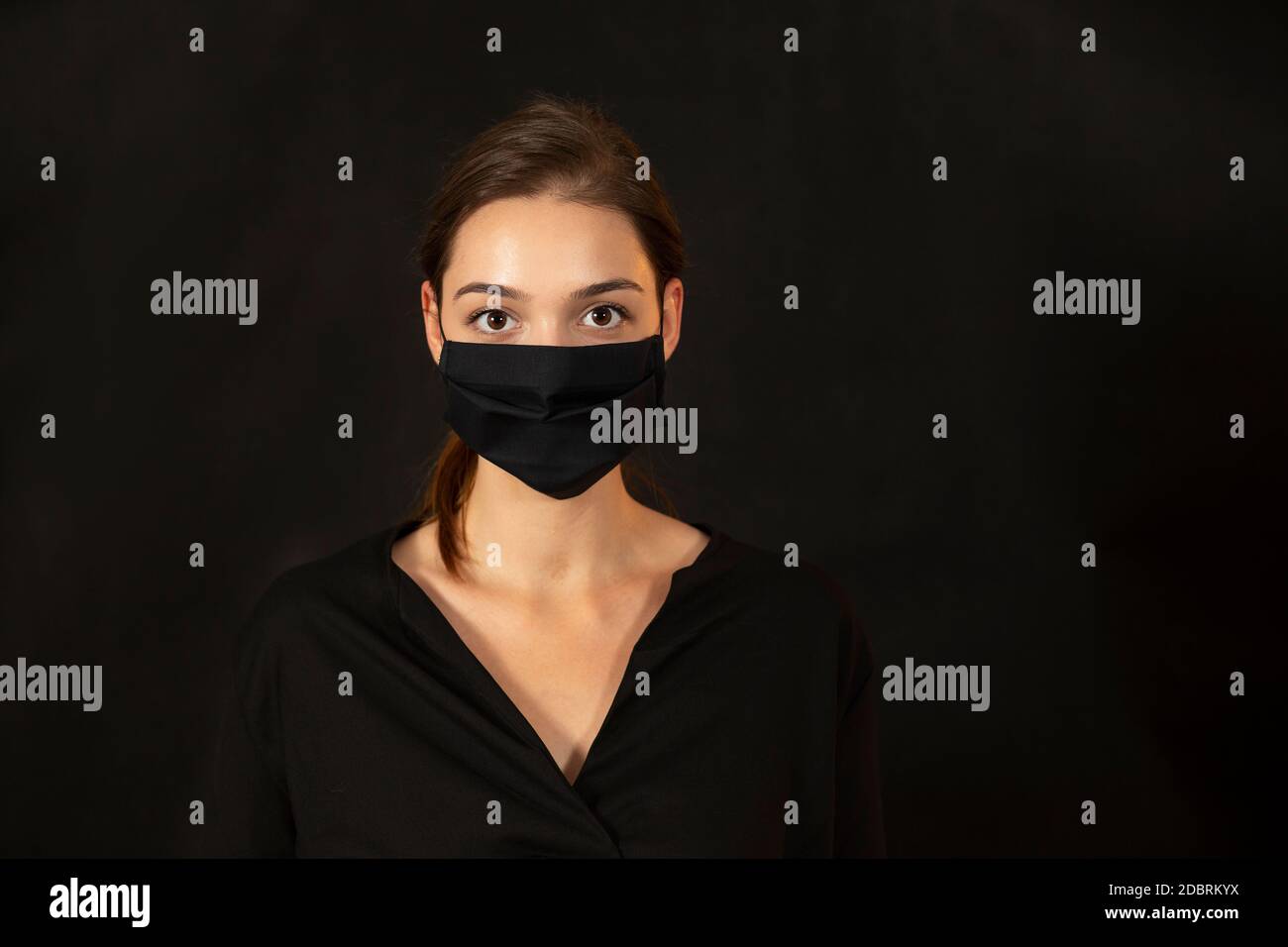 Caucasian girl in black clothes and face protection facing the camera ...