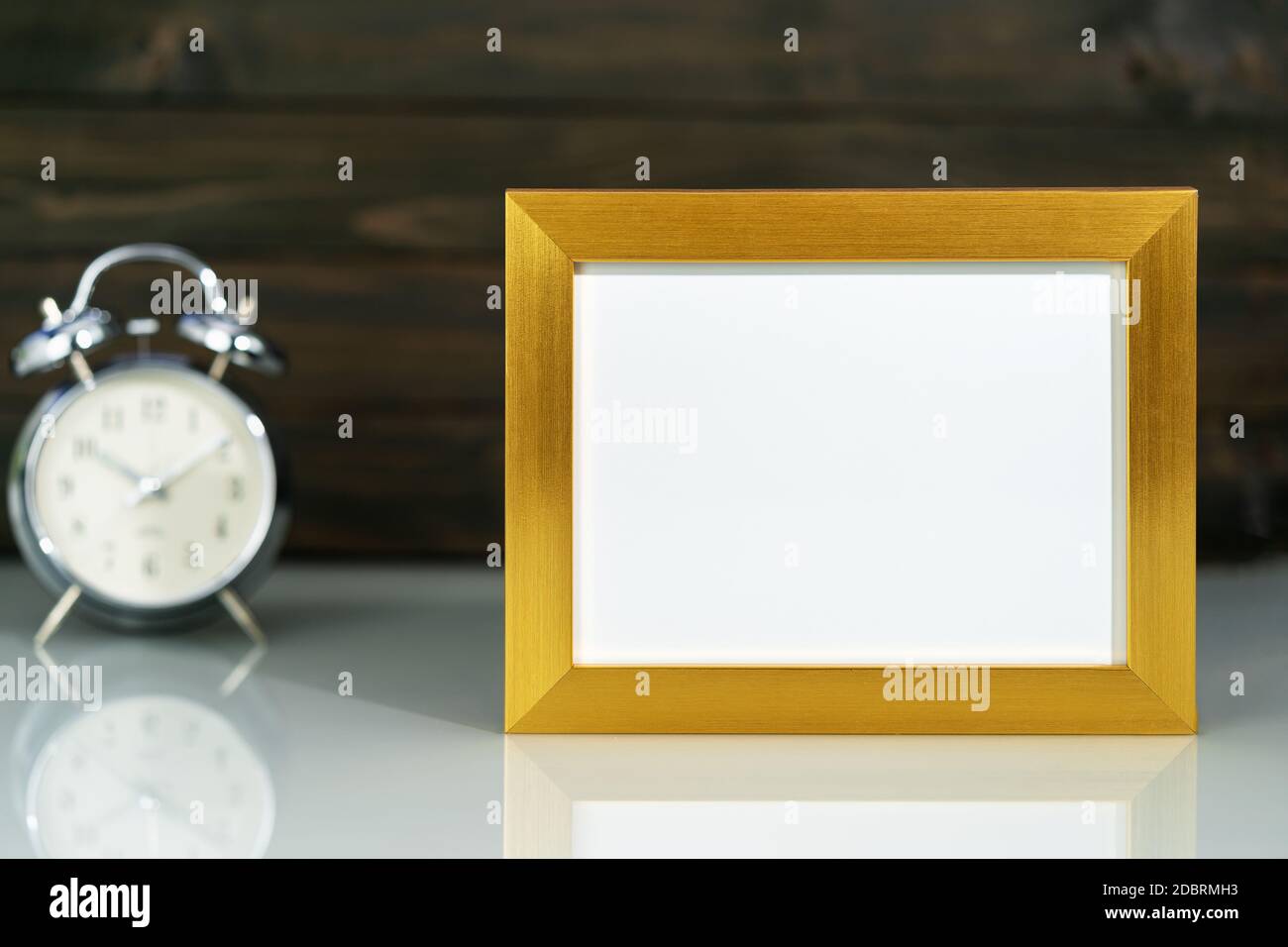 Mockup with blank golden frame and alarm clock on table Stock Photo - Alamy
