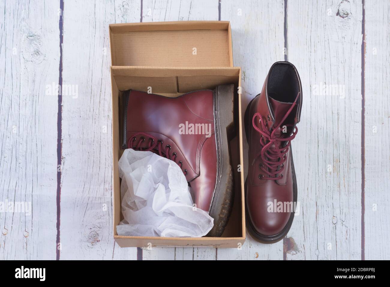 Garnet maroon military boots inside a cardboard box, on a white wooden ...