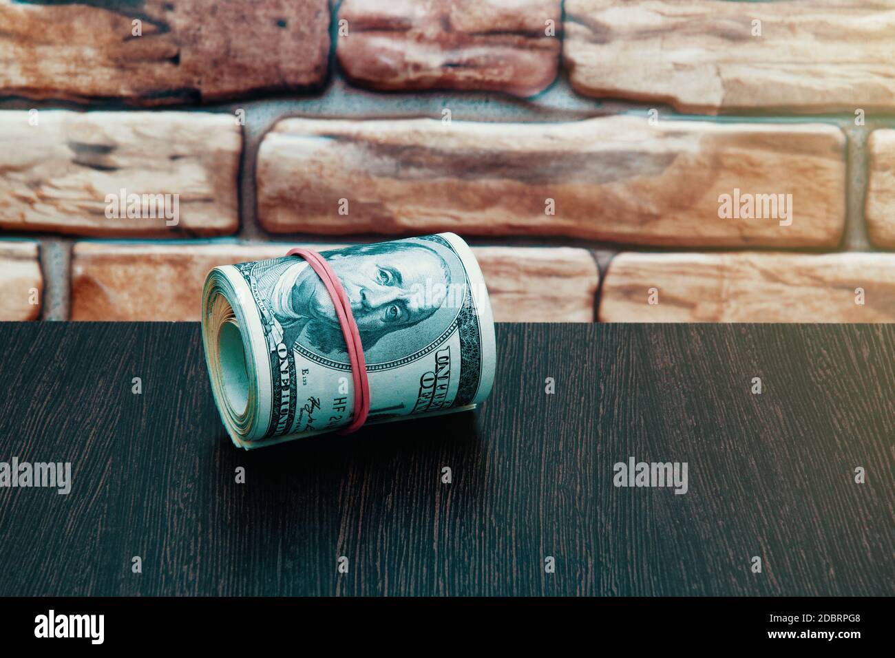A roll of dollars bill.. Close-up, against a brick wall of dark red ...