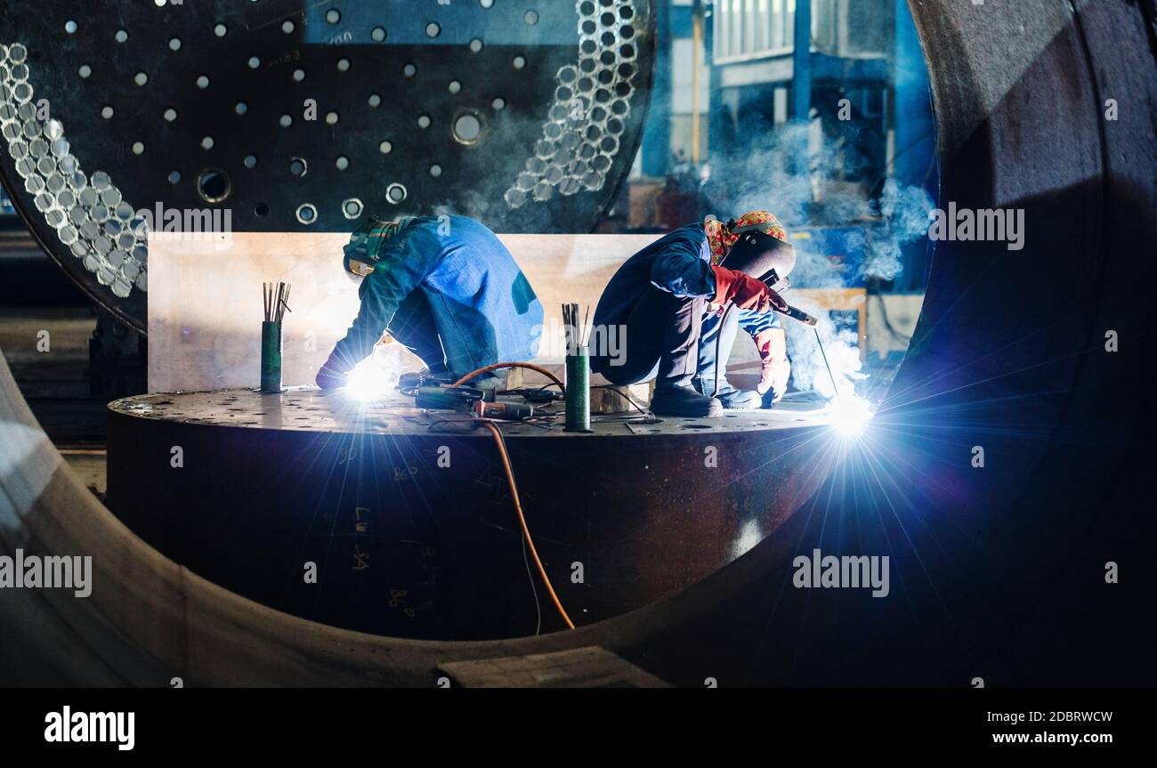 Two workers welding in the interior of a factory manufacturing metallic ...