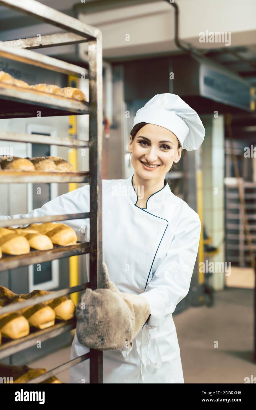 Baker woman pushing sheets with bread in the baking oven wearing bakers ...