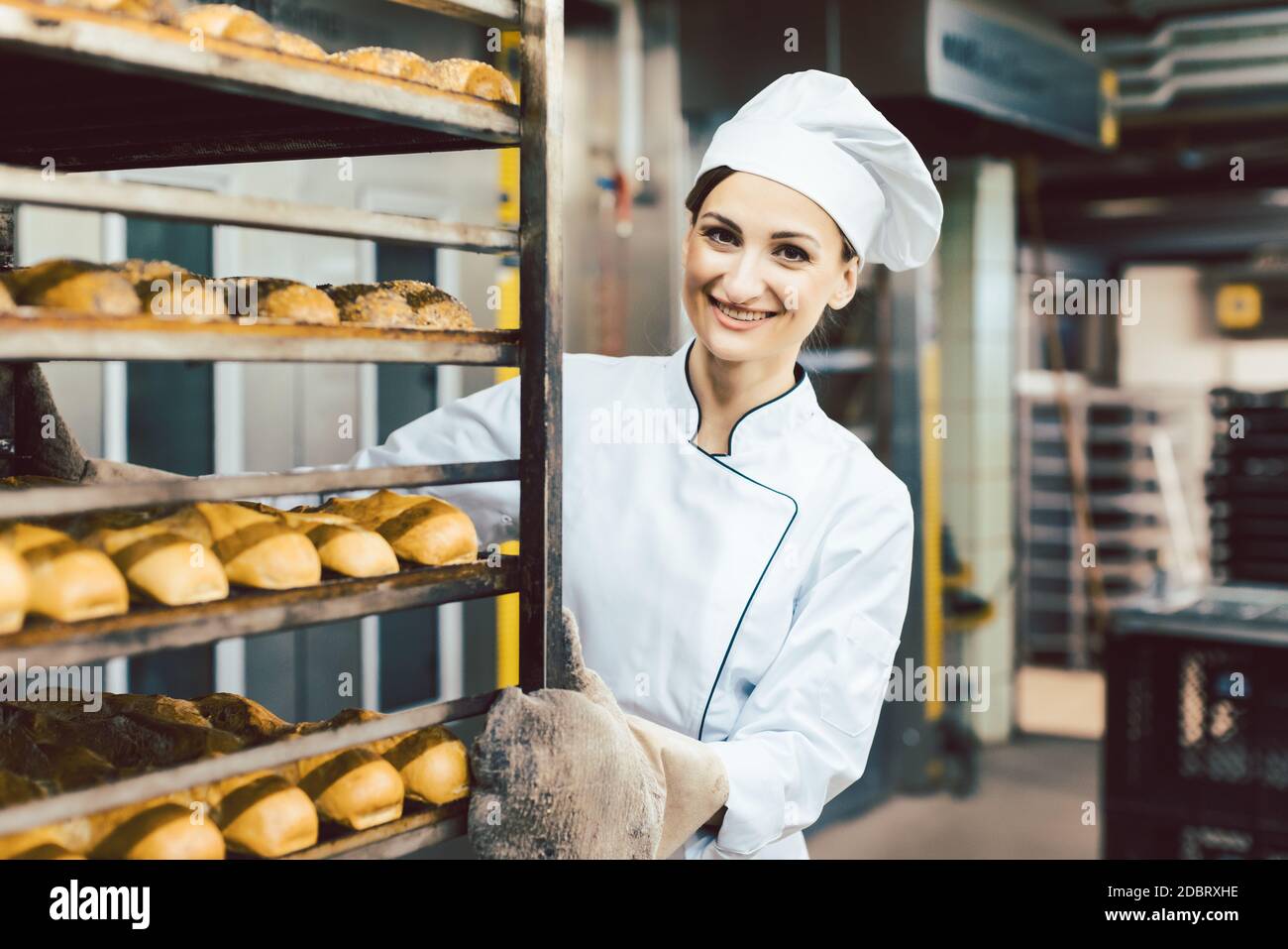 Baker woman pushing sheets with bread in the baking oven wearing bakers ...