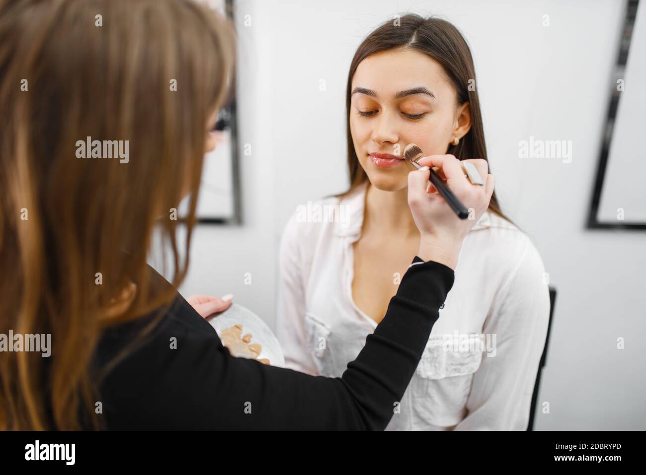 Cosmetologist applies makeup on a woman's face in cosmetics store ...