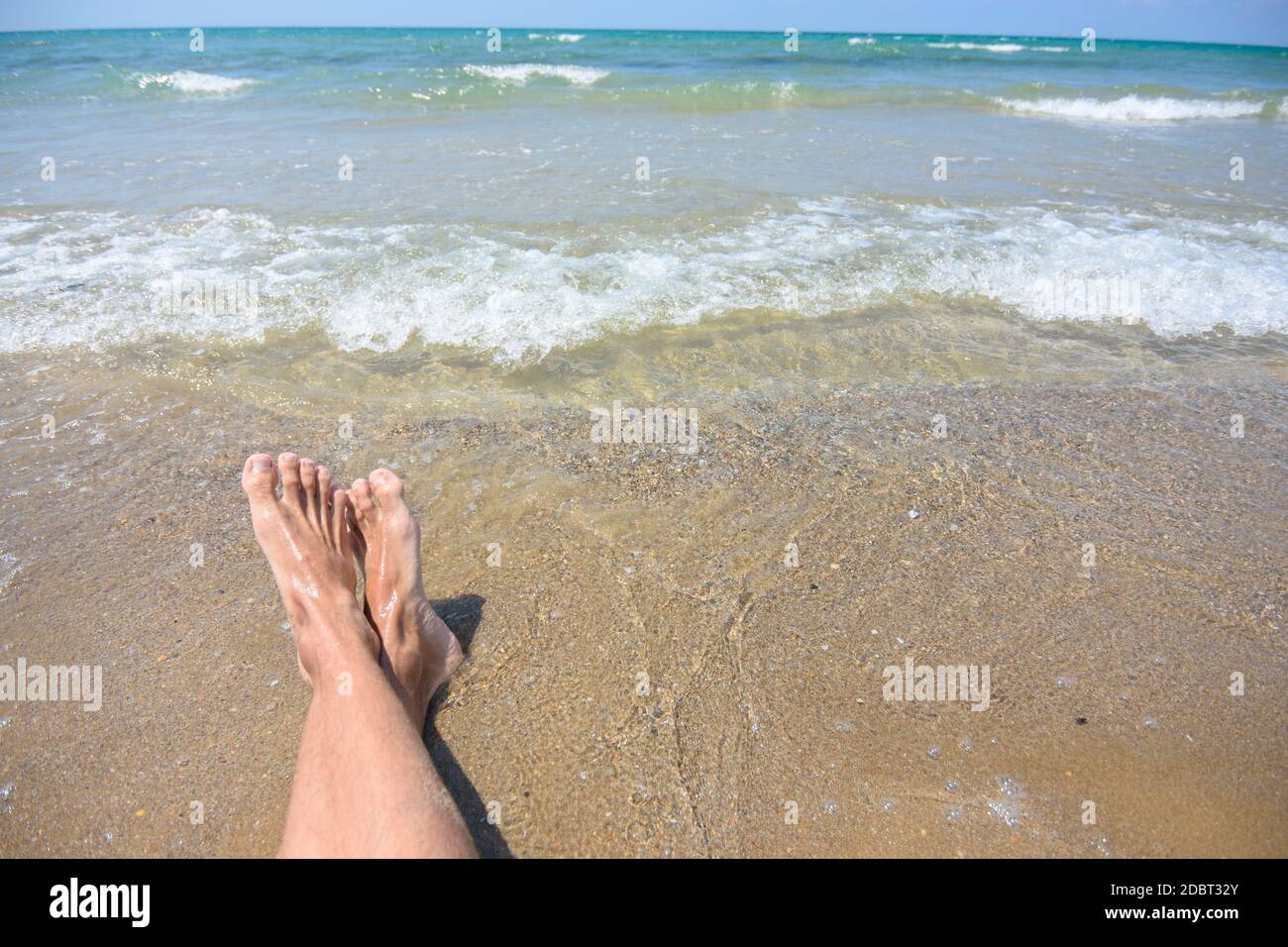 Feet of a man on a sandy beach, in the background a sea surf and ...